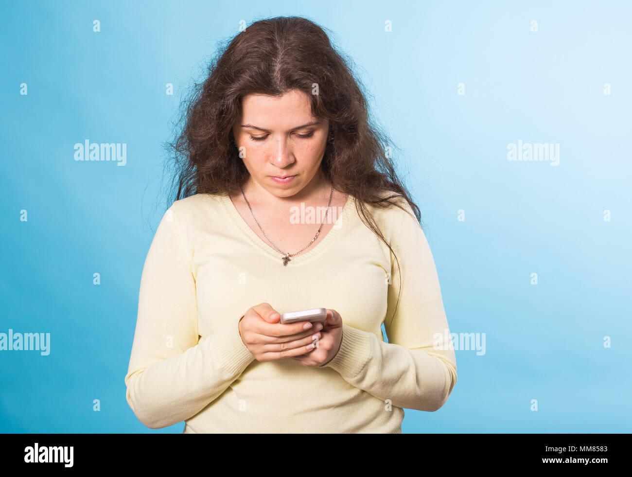 Portrait of a woman sending text message from her phone over blue ...