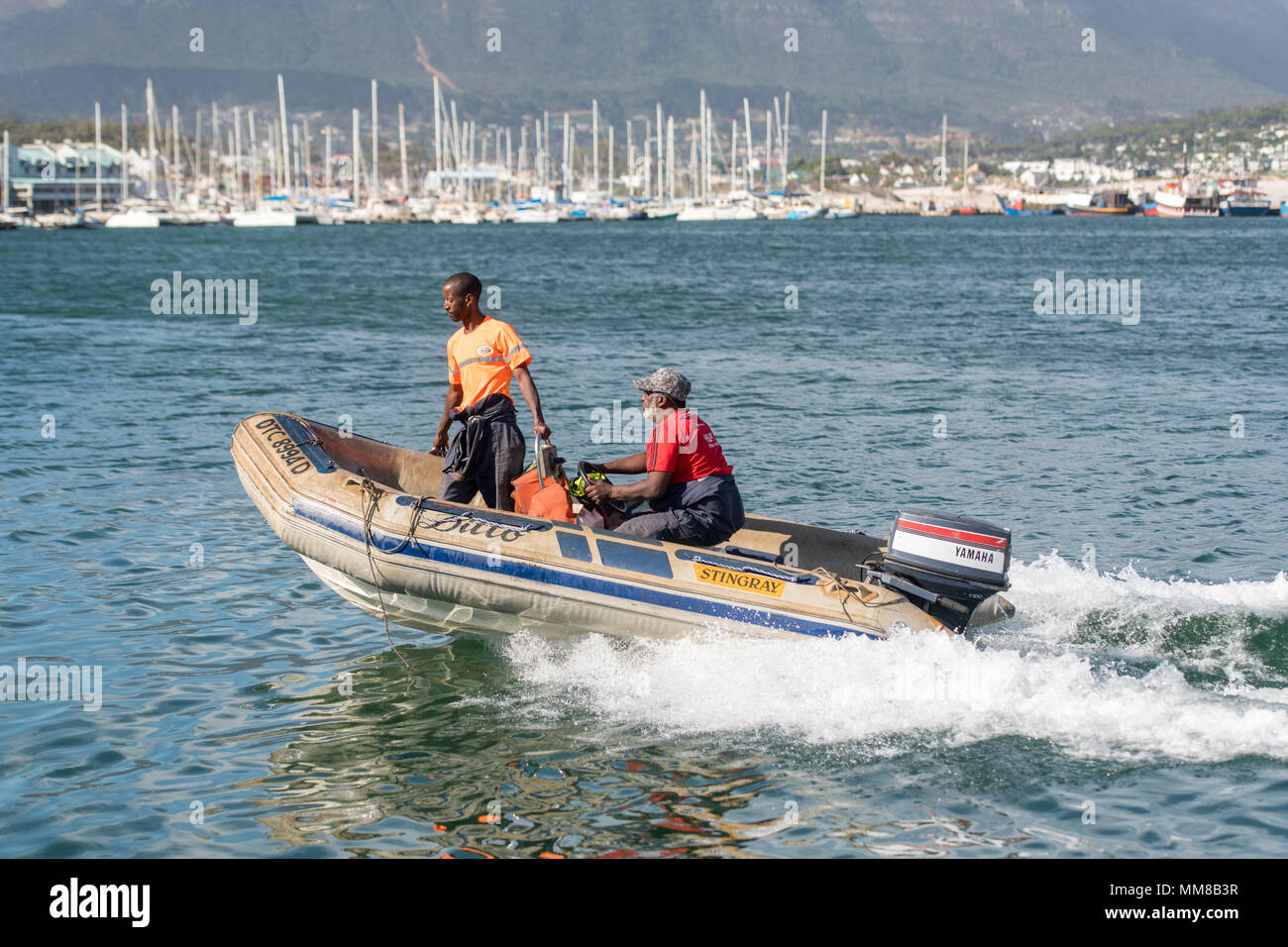 Two men ride a dingy on the water on Hout Bay in Cape Town, South ...