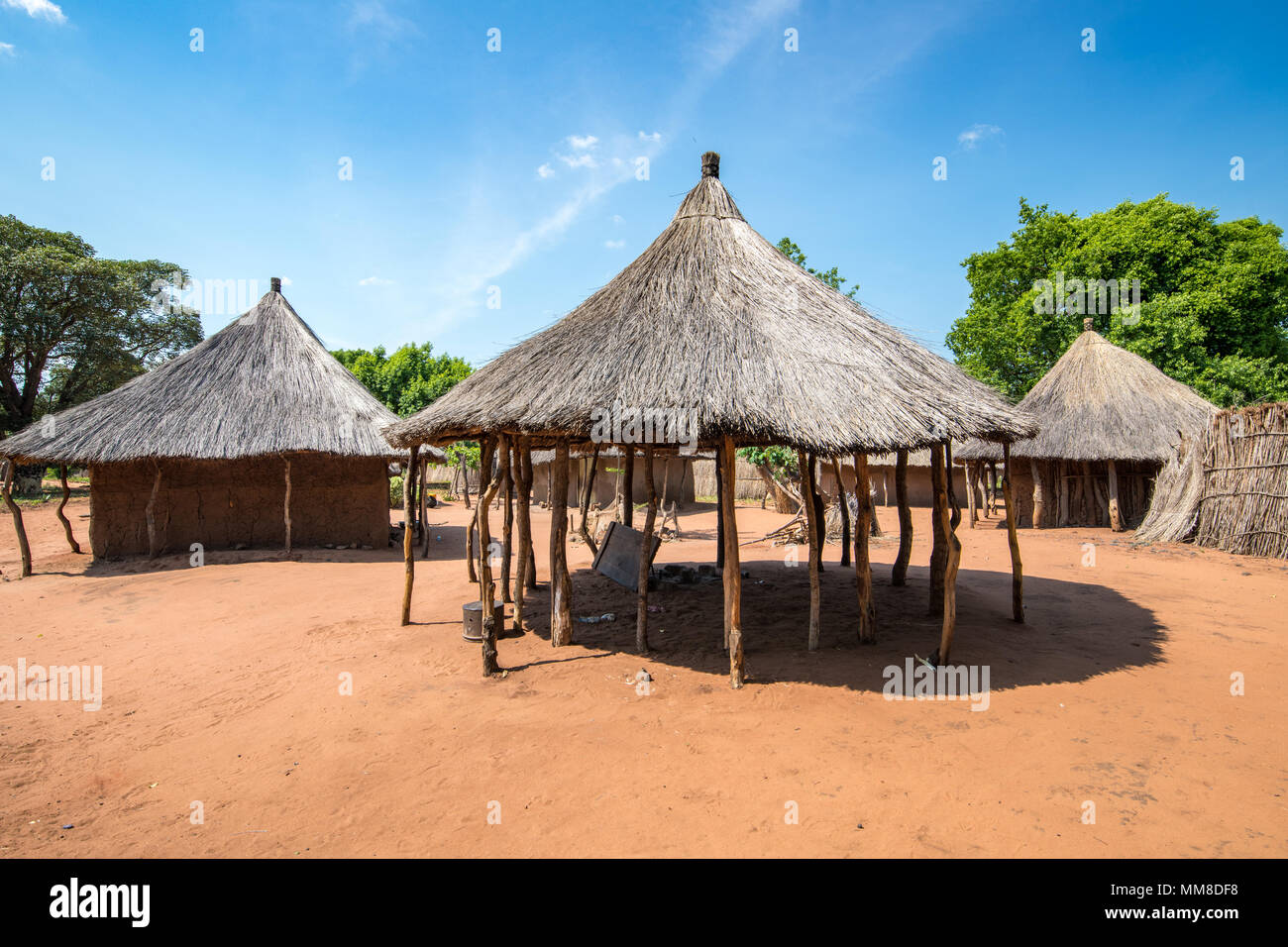 Cluster of huts with thatched roofs inside of Mukuni Village with blue ...
