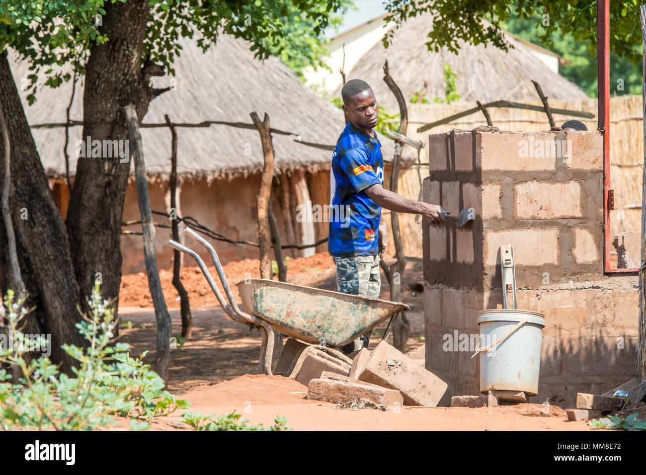 Zambian man constructing building uses mud to seal together stone ...
