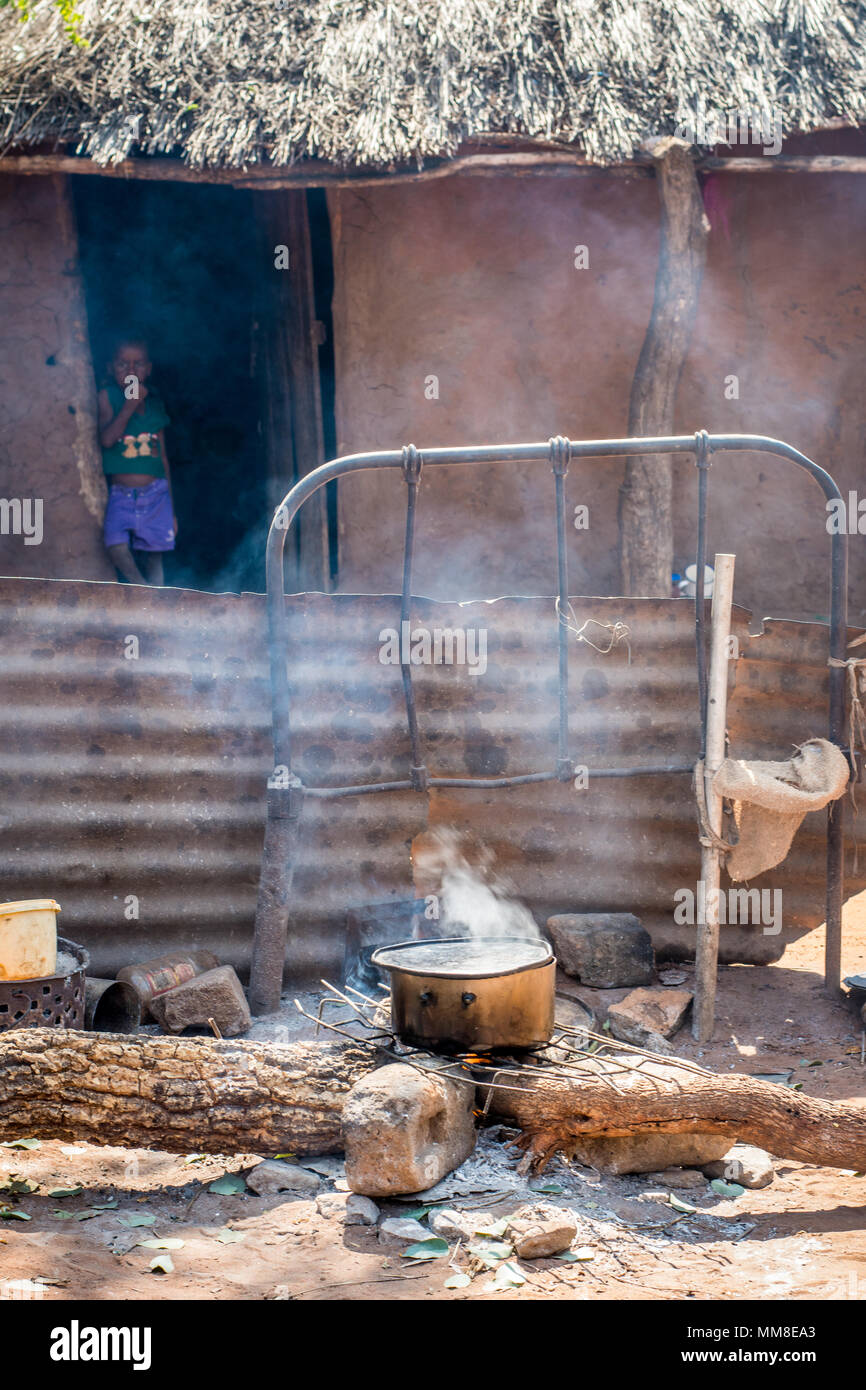 Metal cooking pot sits on grate on top of campfire with thatched hut ...
