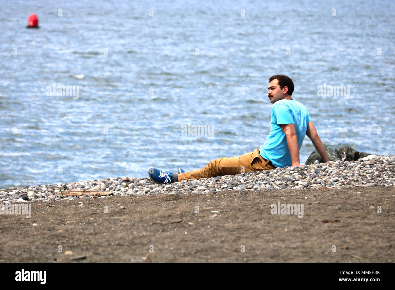 Man sitting on the beach very close to the waters edge of Bellingham ...