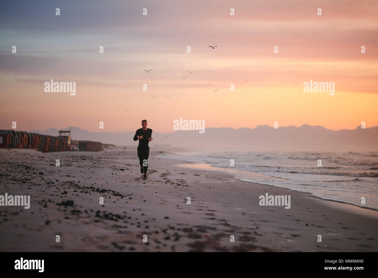 Full length shot of fit male runner running on the beach in morning ...