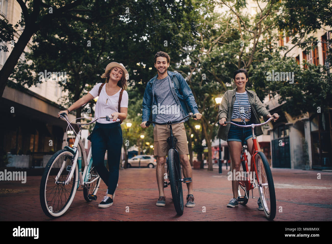 Full length of three young people with their bicycles on city street ...