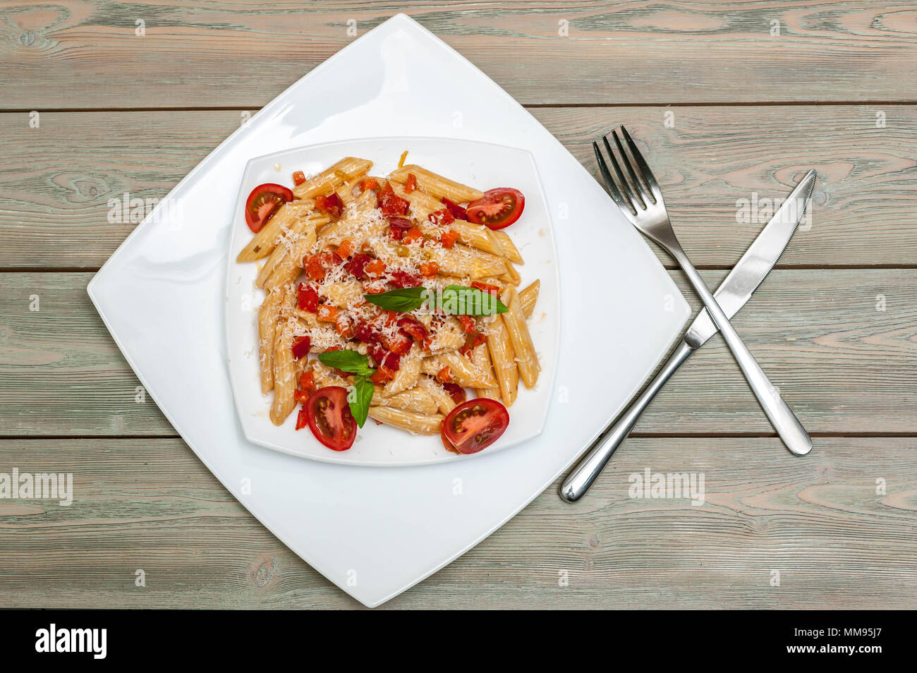 Penne pasta with vegetables and parmesan cheese on a white square plate ...