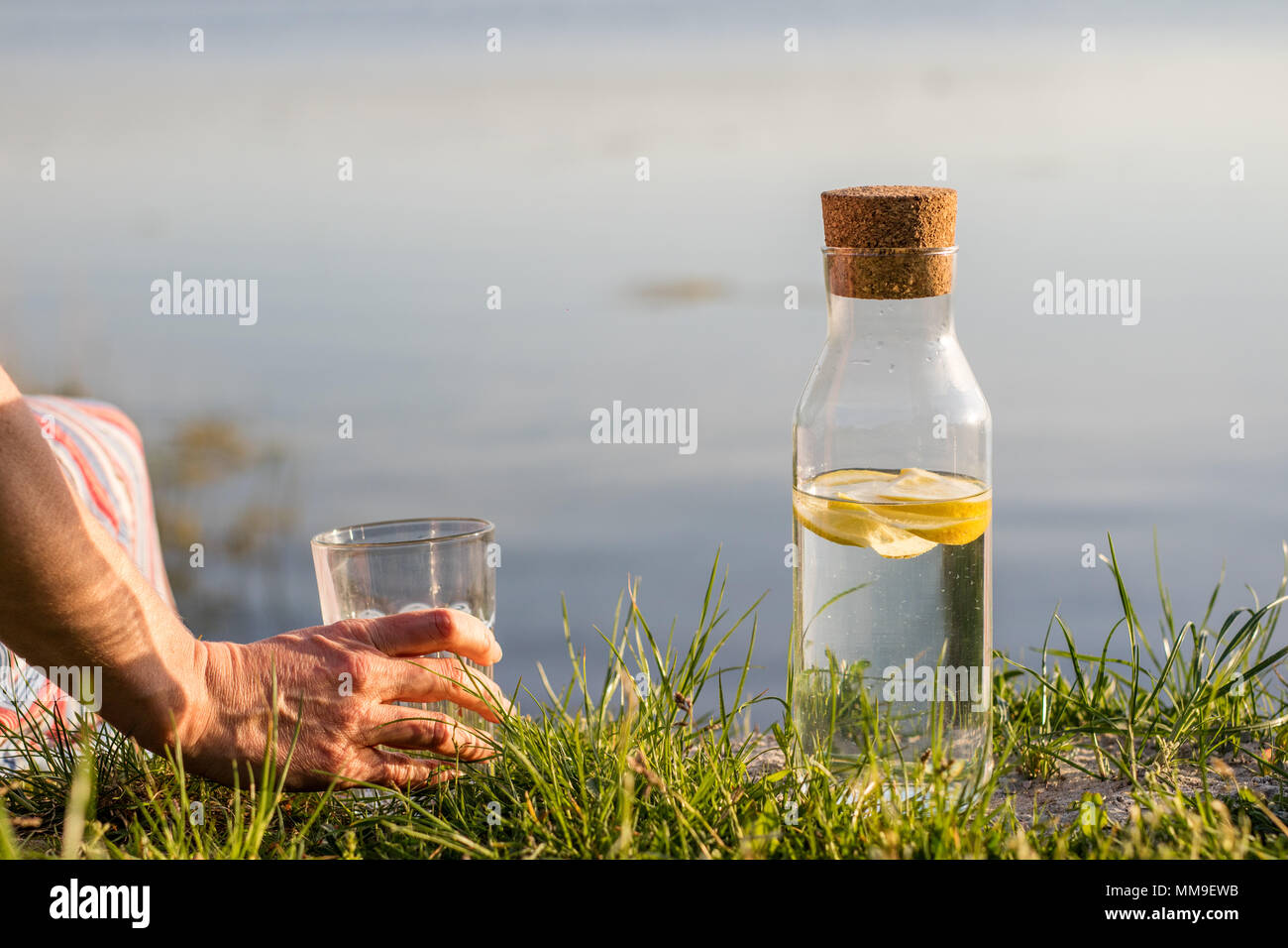 A bottle of water with lemon and a glass. A woman drinking water from ...
