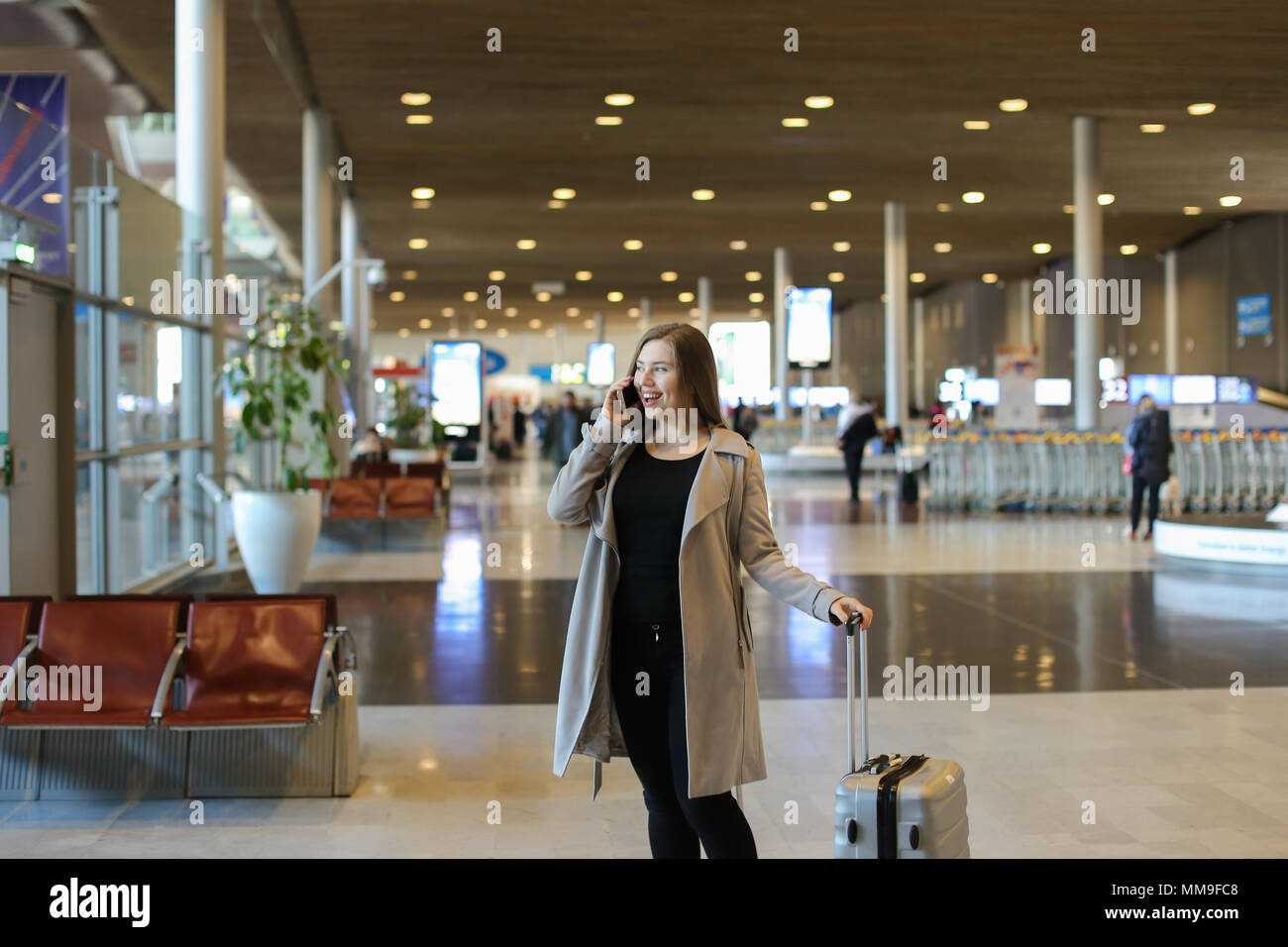 Pretty girl going in airport hall with valise and talking by smartphone ...