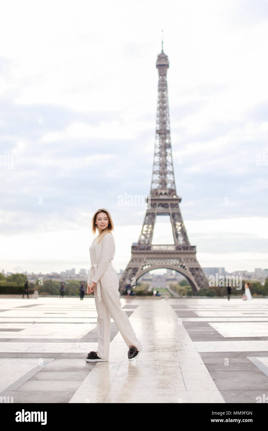 Stylish jocund woman standing near Eiffel Tower in white overalls Stock ...