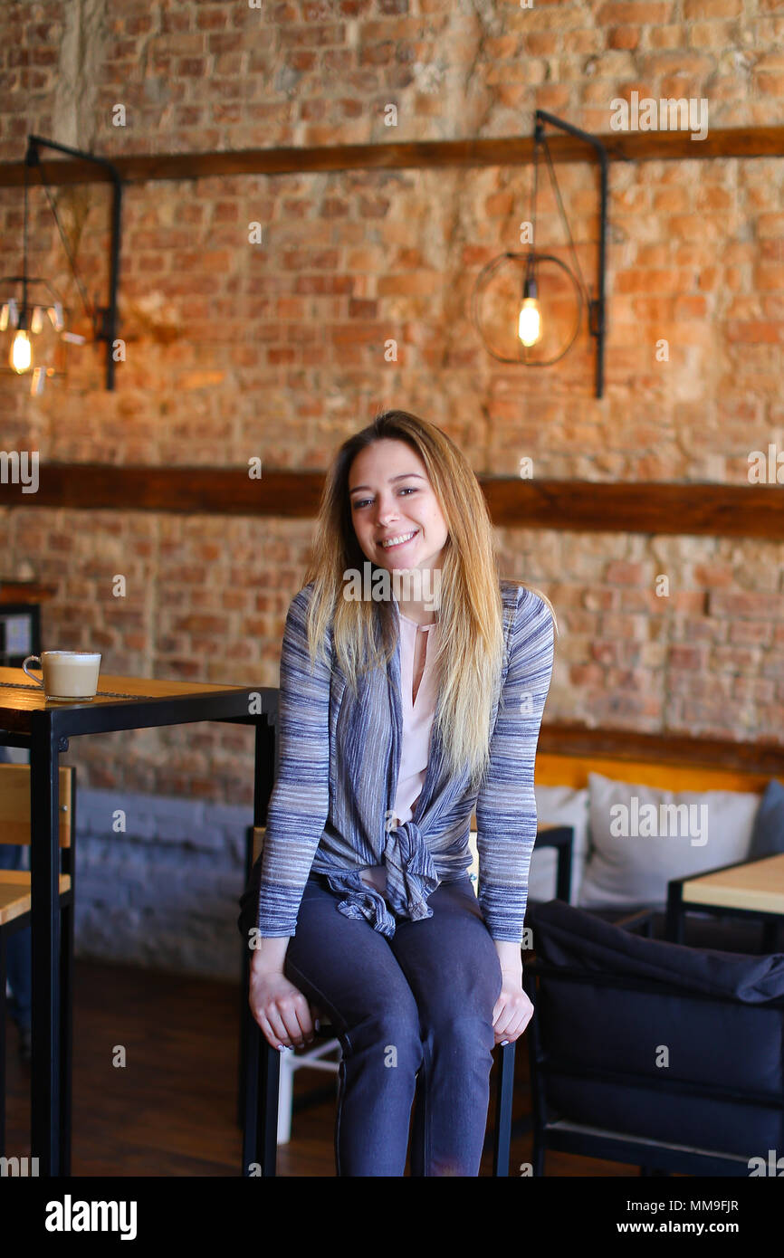 Satisfied girl sitting near table in cozy cafe with unusual interior ...