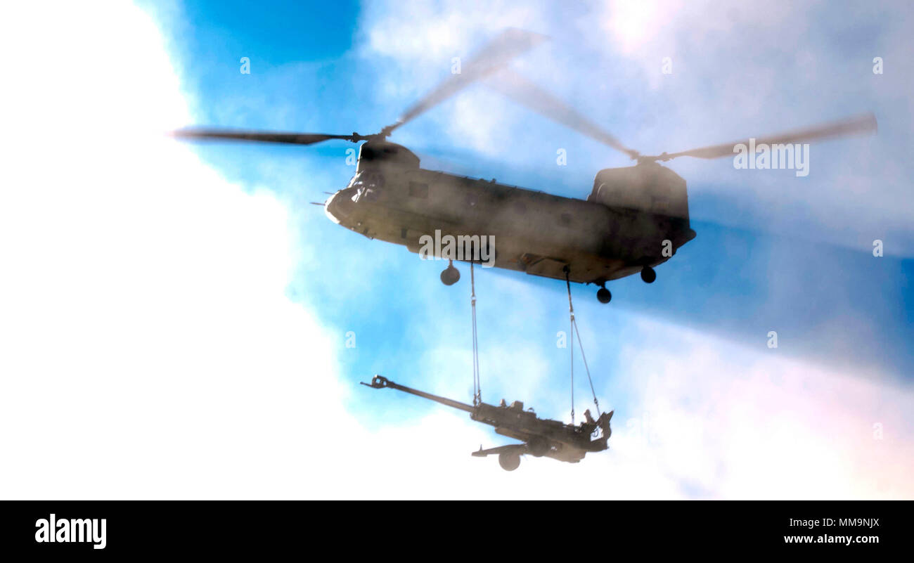 A Chinook helicopter carrying a sling loaded M777A2 howitzer cuts through the dusty skies during ...