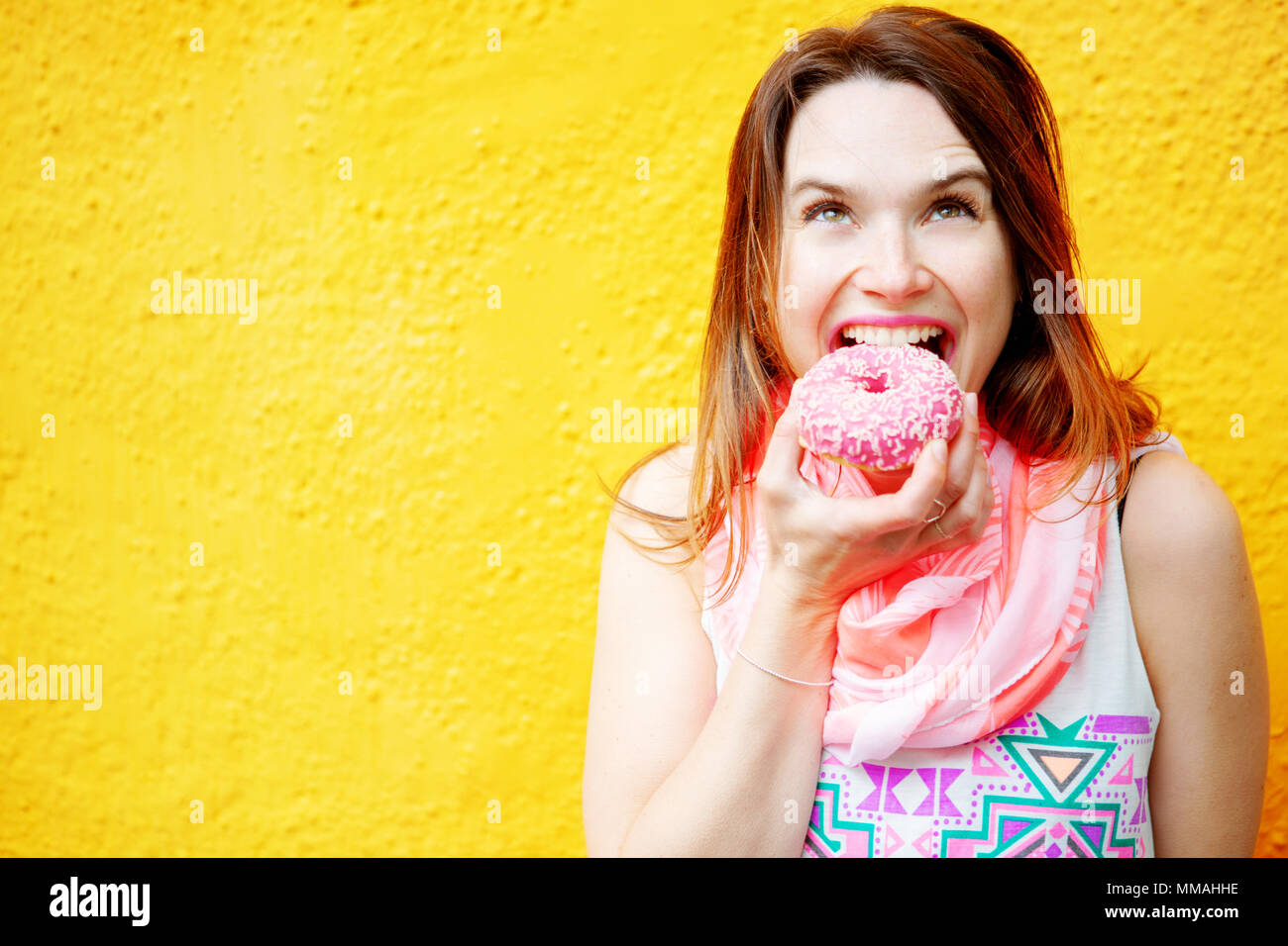 young brunette woman eating a donut in front of yellow background Stock ...