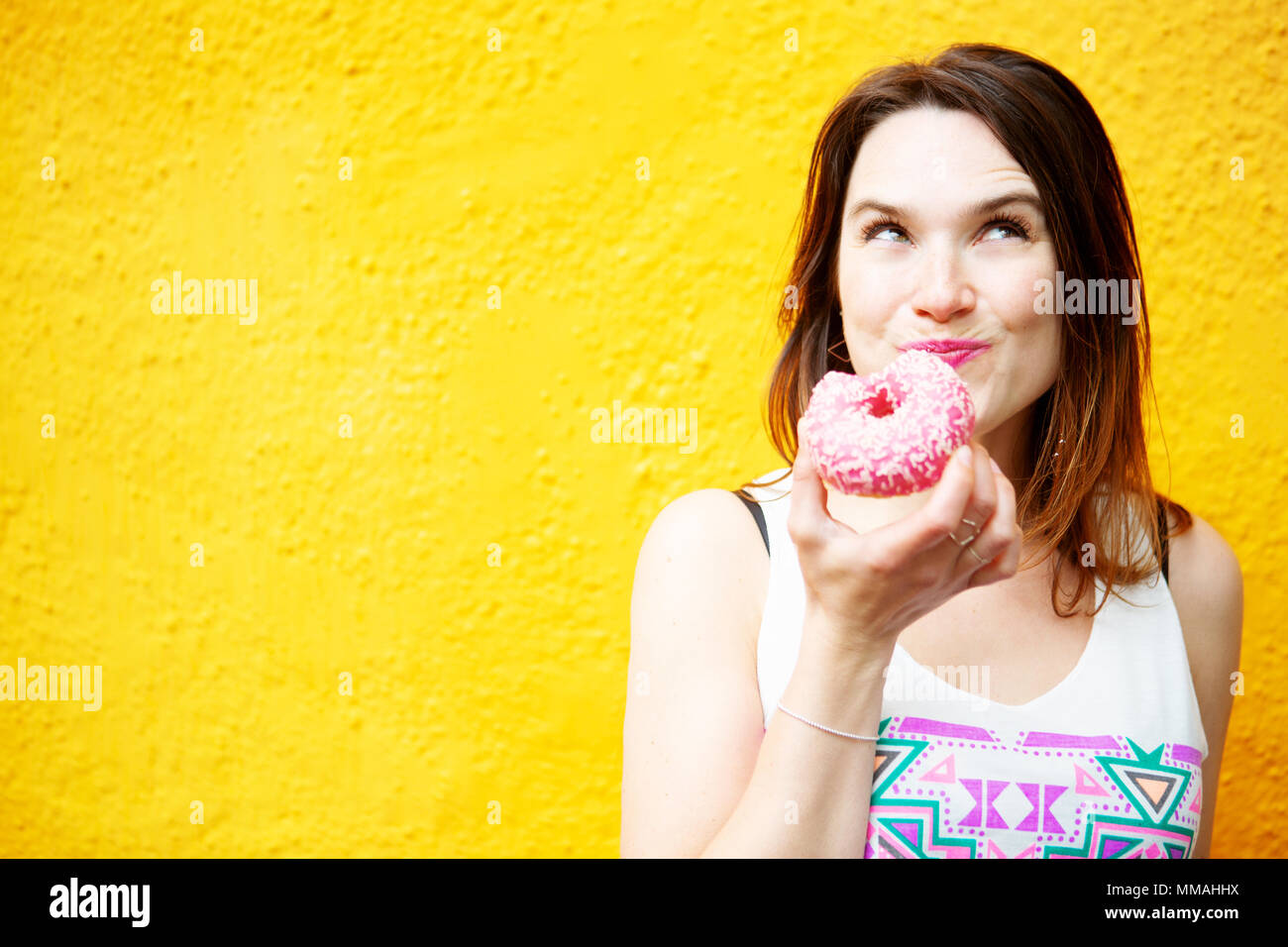 young brunette woman eating a donut in front of yellow background Stock ...