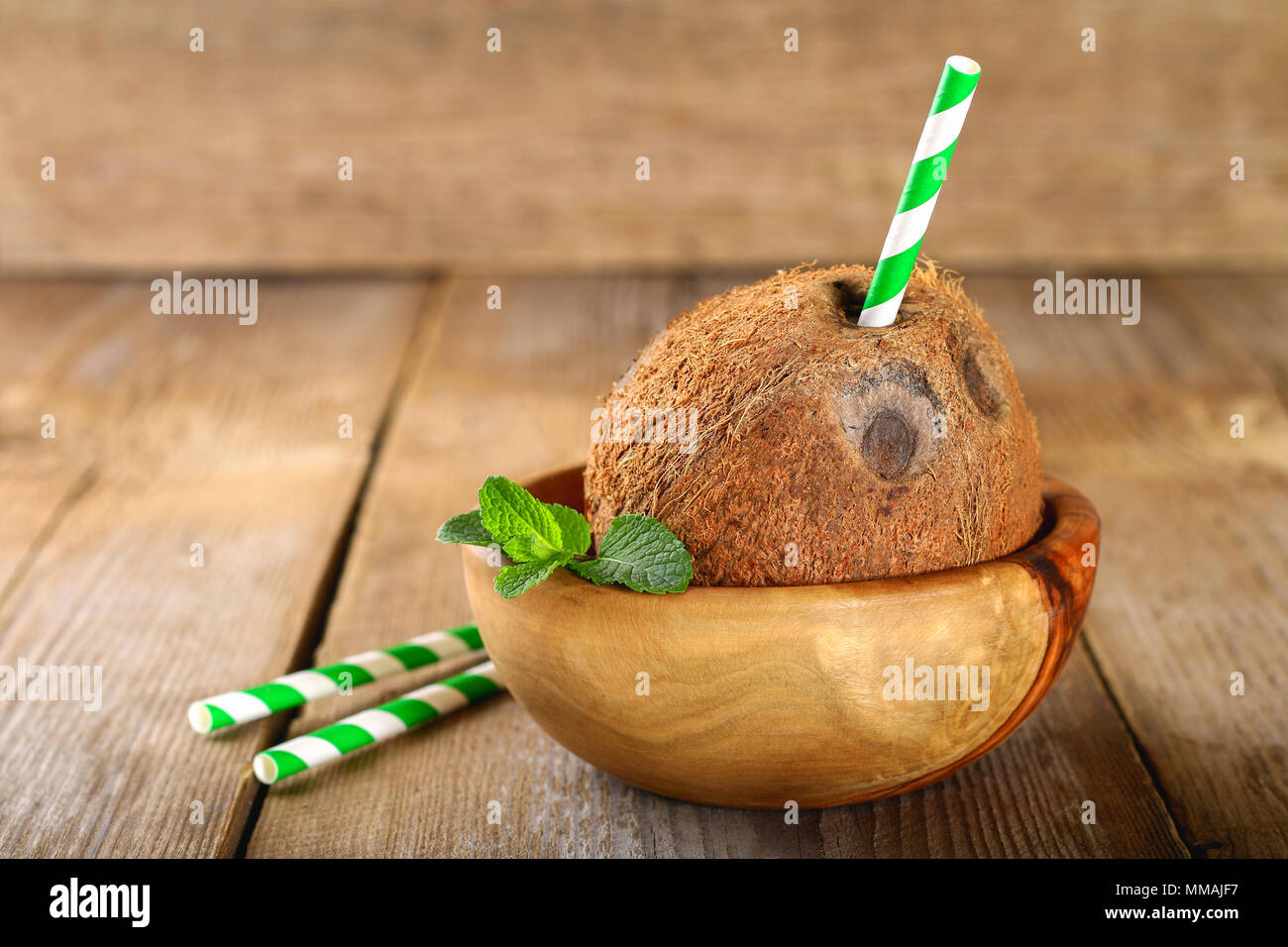 Coconut with juice inside, mint and green paper tubes on an old wooden ...