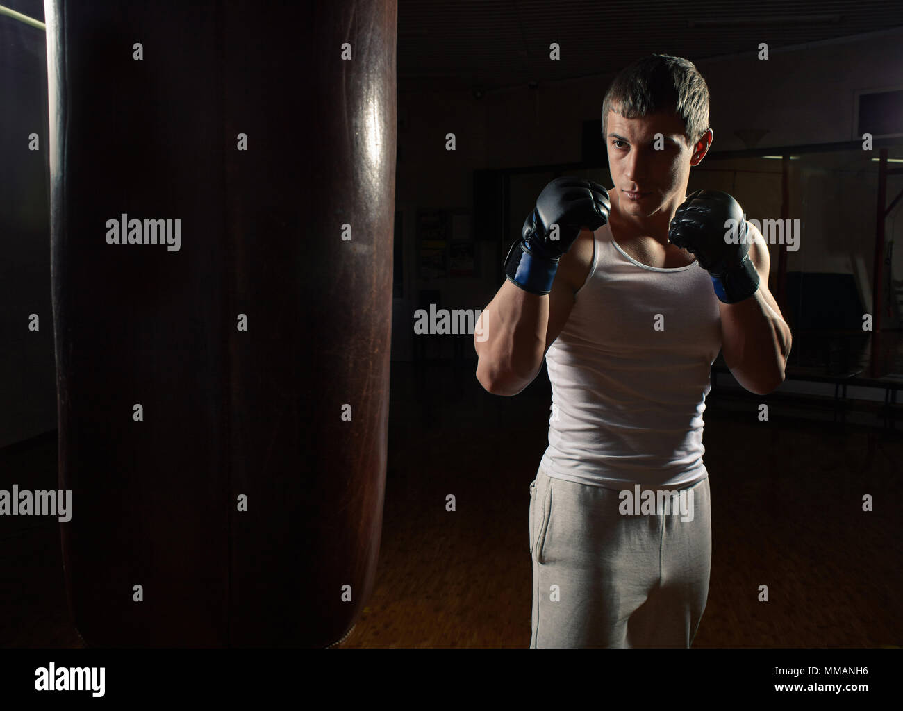 young muscular man boxer workout with punching bag in dark interior ...