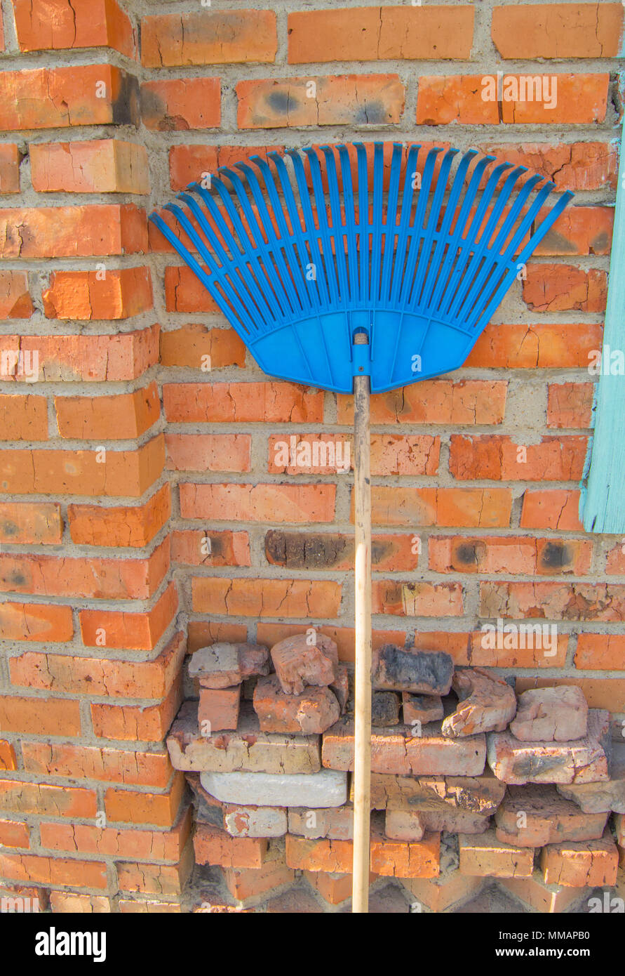 Blue plastic rake for harvesting leaves and grass are near the red ...