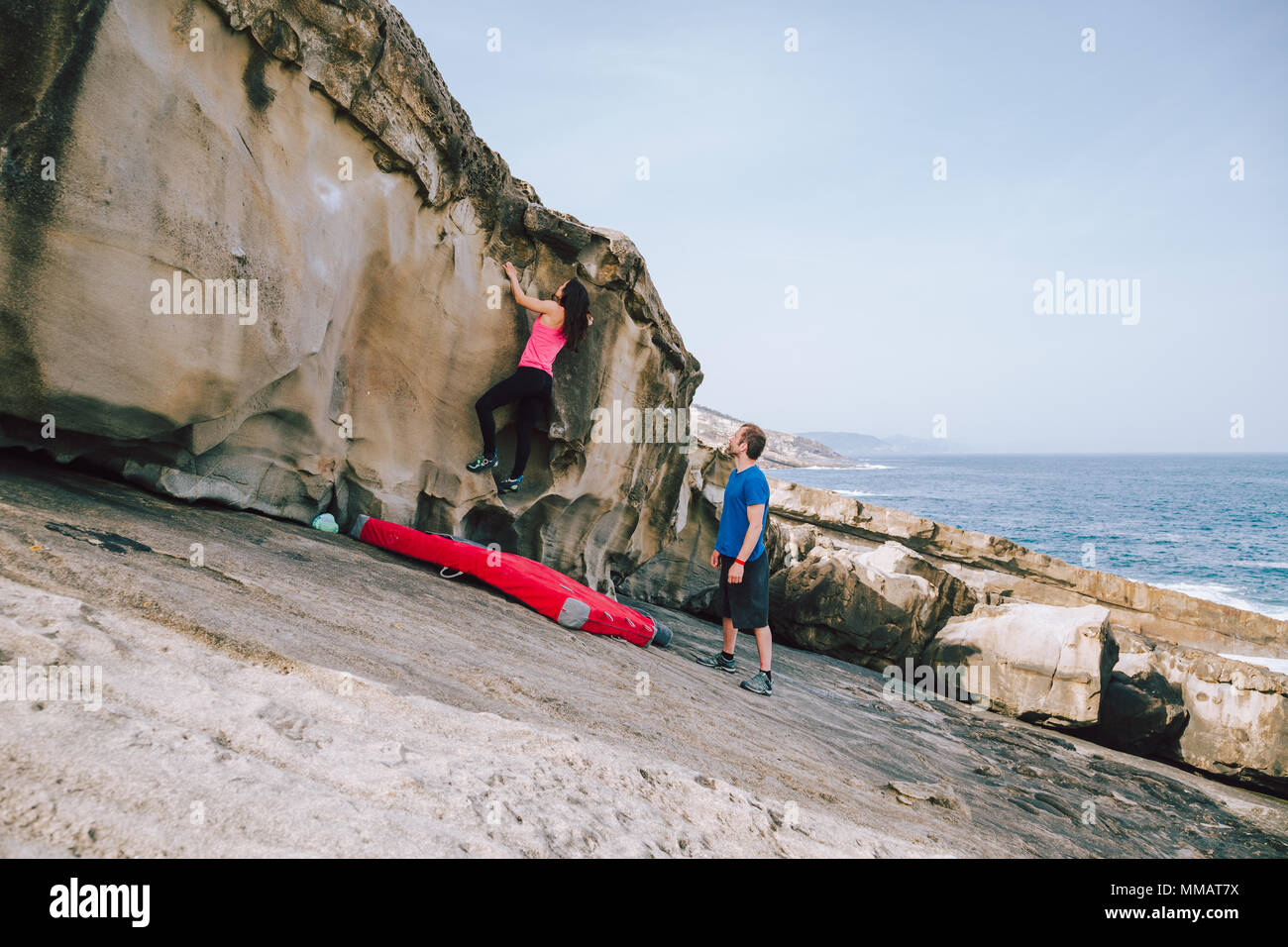 Young couple of climbers assisting eachother to climb the cliff in the ...