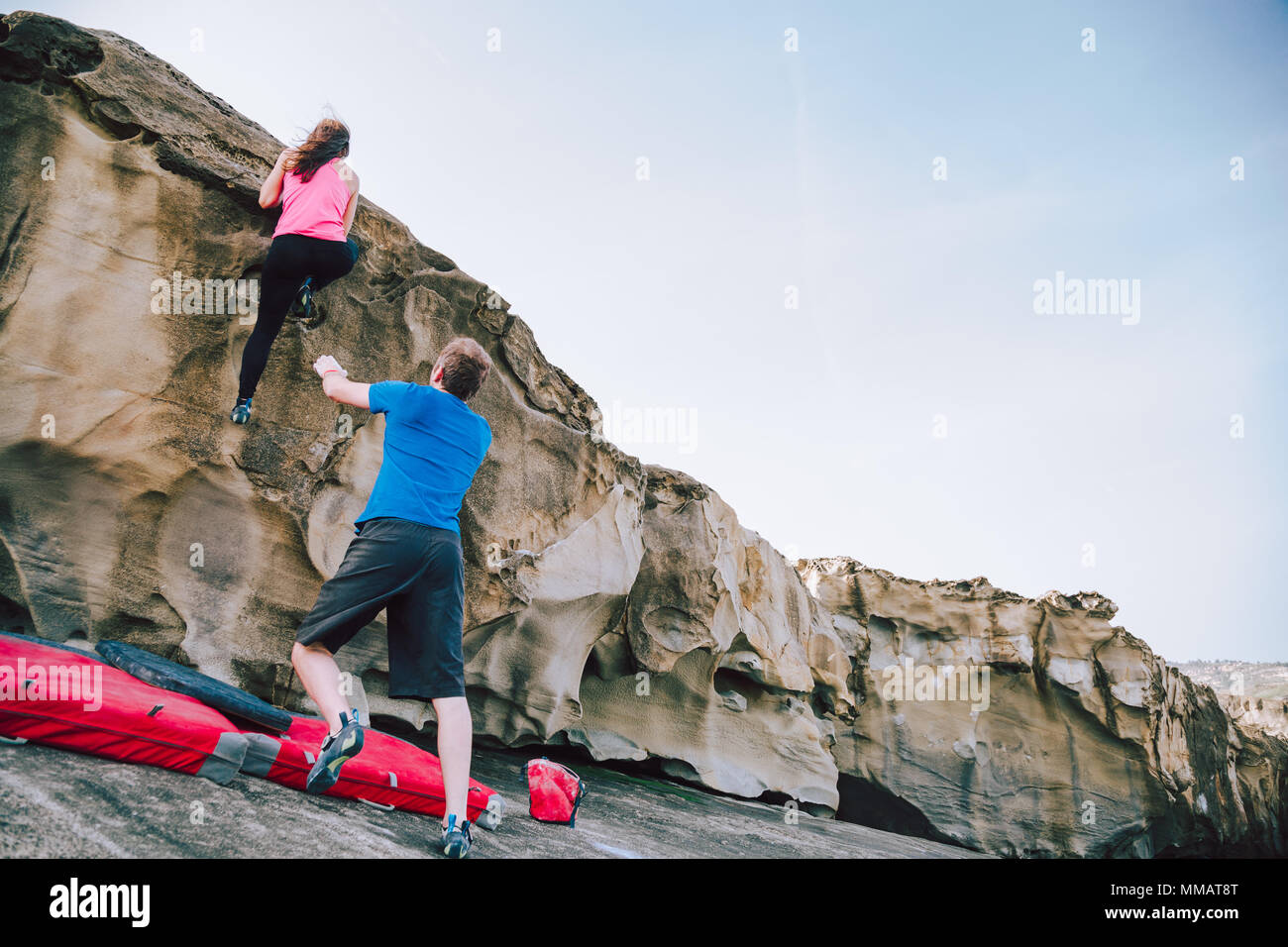 Young couple of climbers assisting eachother to climb the cliff in the ...