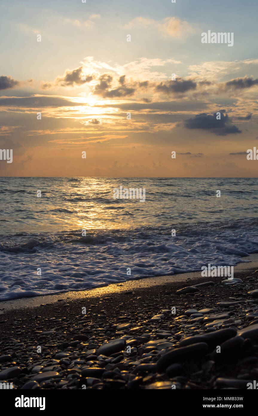 Summer sea sunset on the pebble beach, the sun, waves and clouds ...