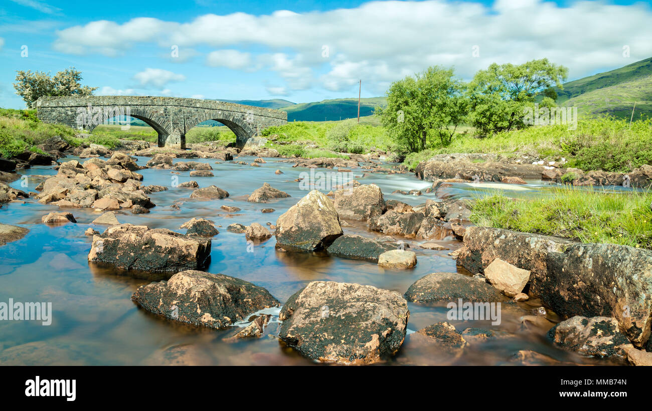 Low angle shot of an old bridge spanning a river into Loch Scridain the ...