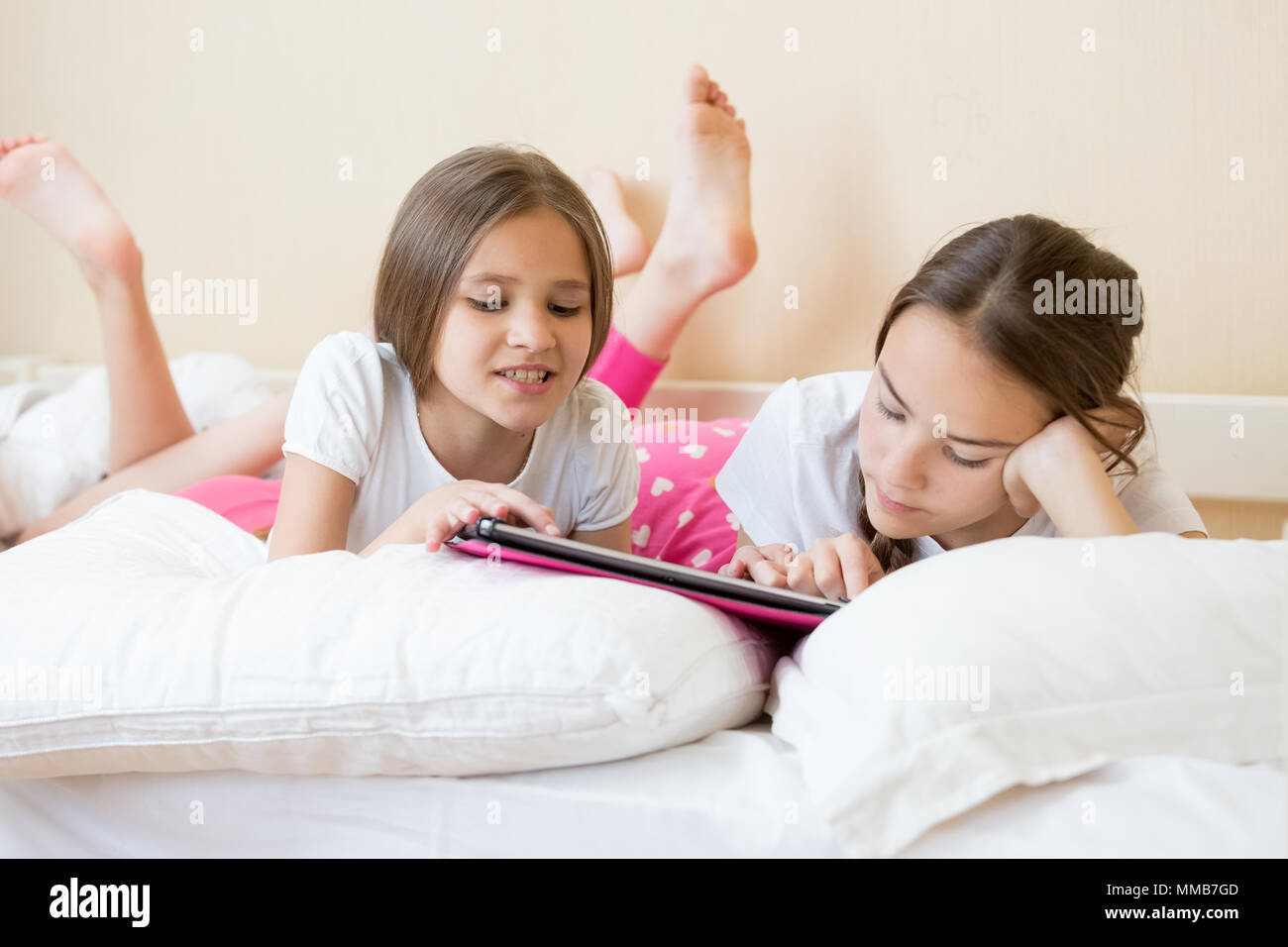 Closeup portrait of two teenage sisters using tablet computer on bed ...