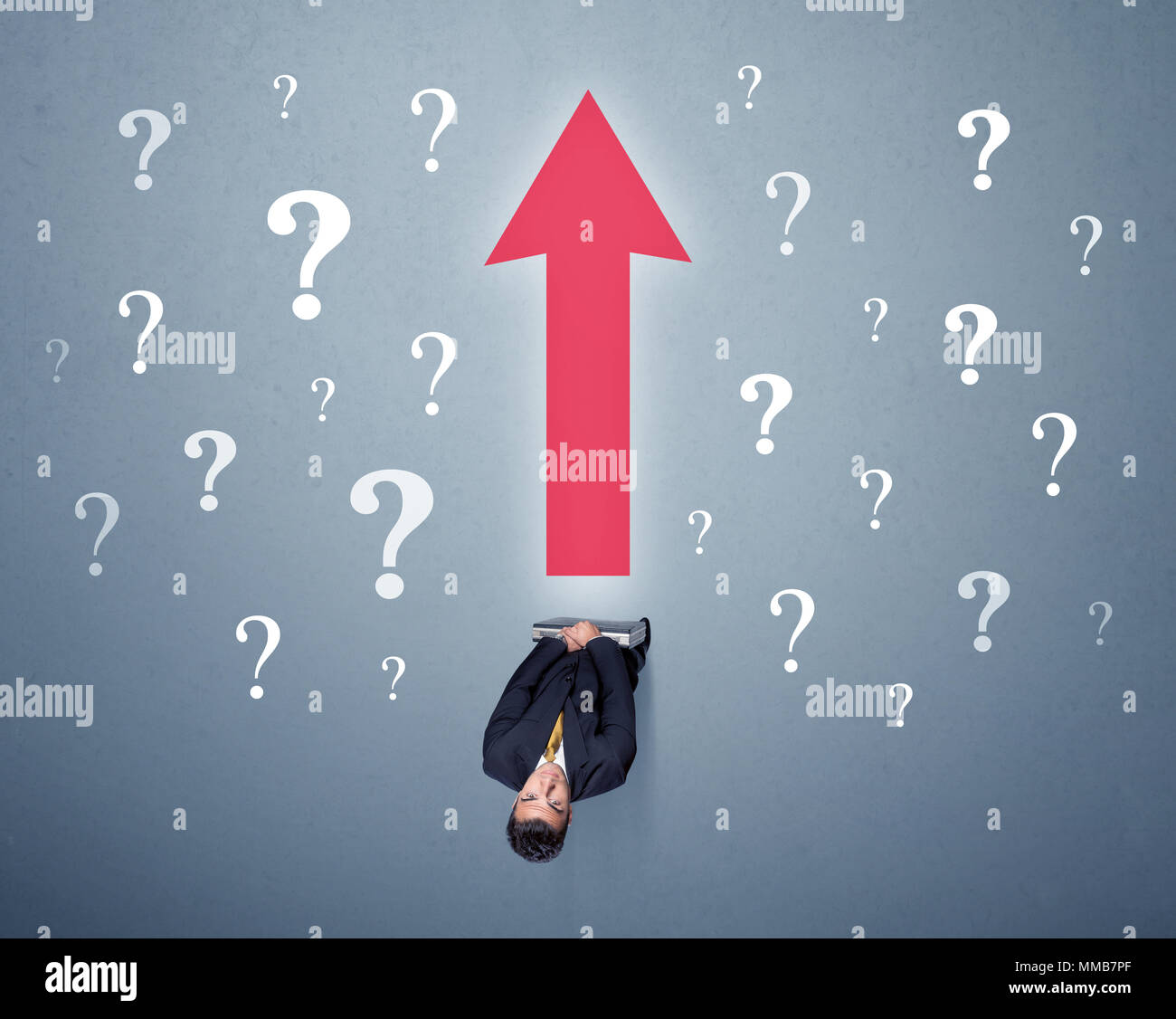 Young contemplating businessman stands in front of a big red arrow and ...