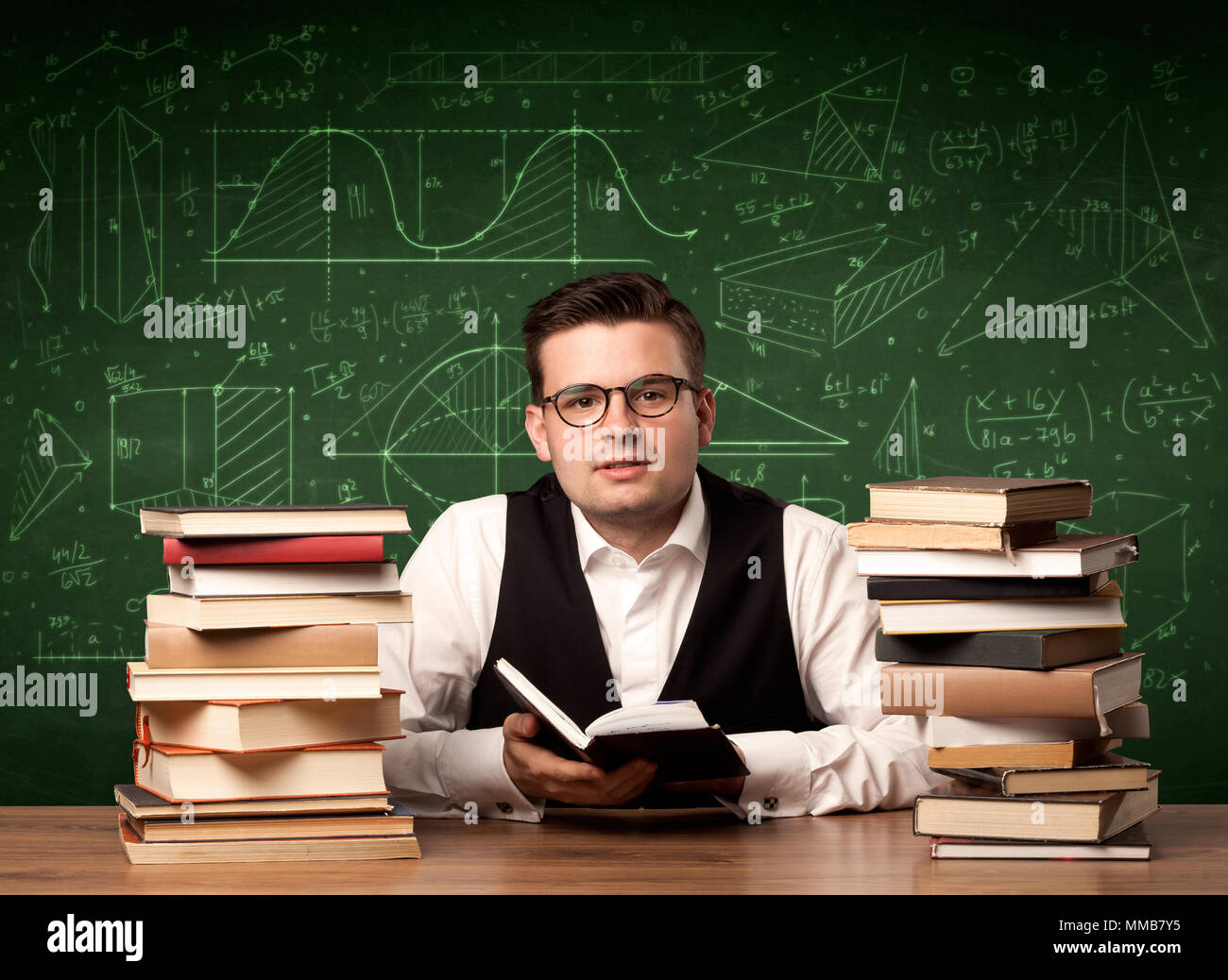 A young passionate male teacher sitting at school desk, reading a book ...