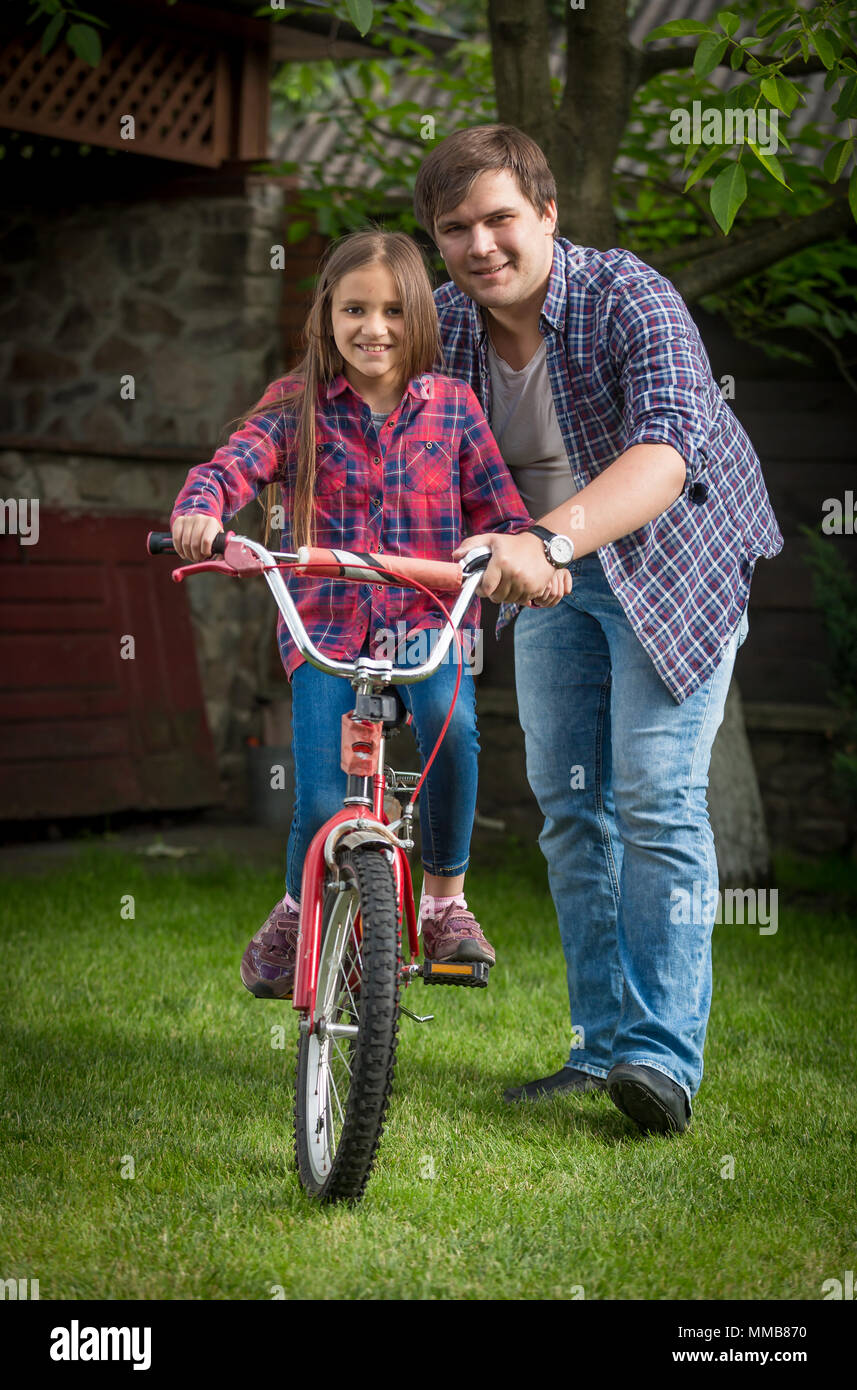 Portrait of smiling young man pushing his daughter learning how to ride ...