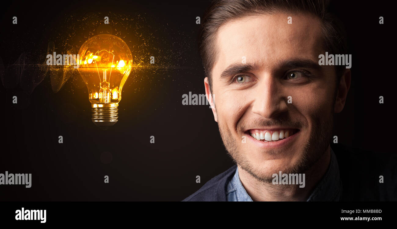 Portrait of a young businessman with a lightbulb next to him on a dark ...