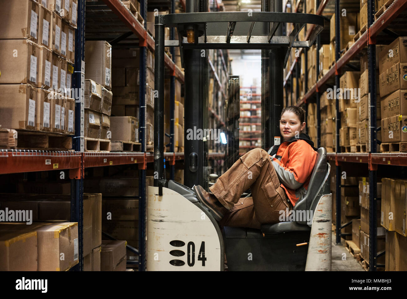 Caucasian female warehouse worker sitting in a motorized stock picker ...