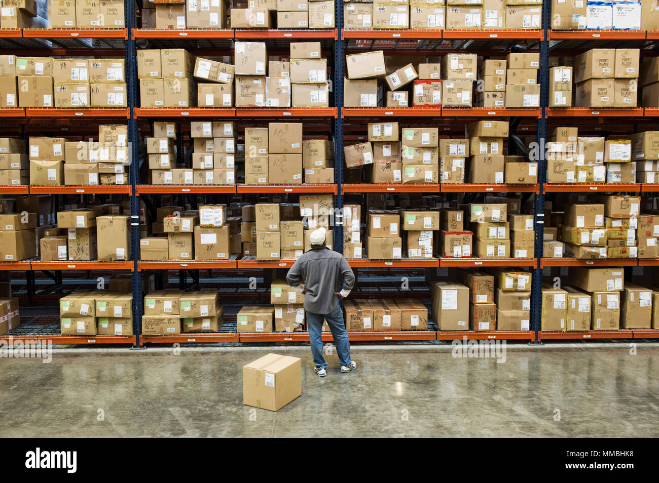 Warehouse worker checking inventory next to large racks of cardboard ...