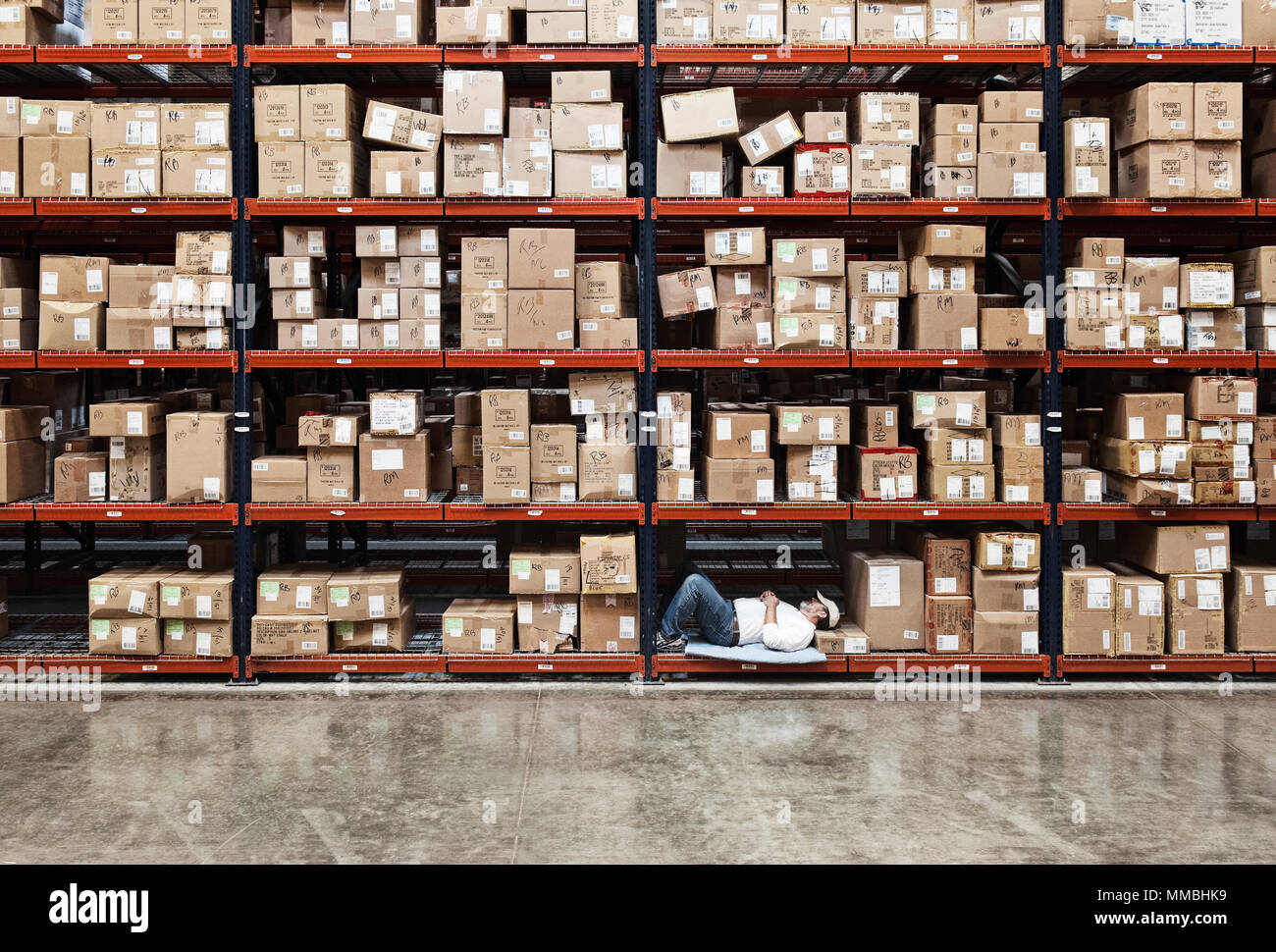 Warehouse worker taking a break next to large racks of cardboard boxes ...