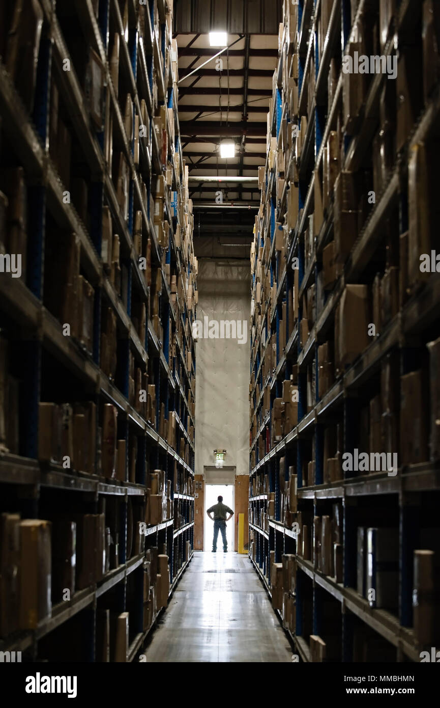 Single warehouse worker in between large racks of cardboard boxes on ...