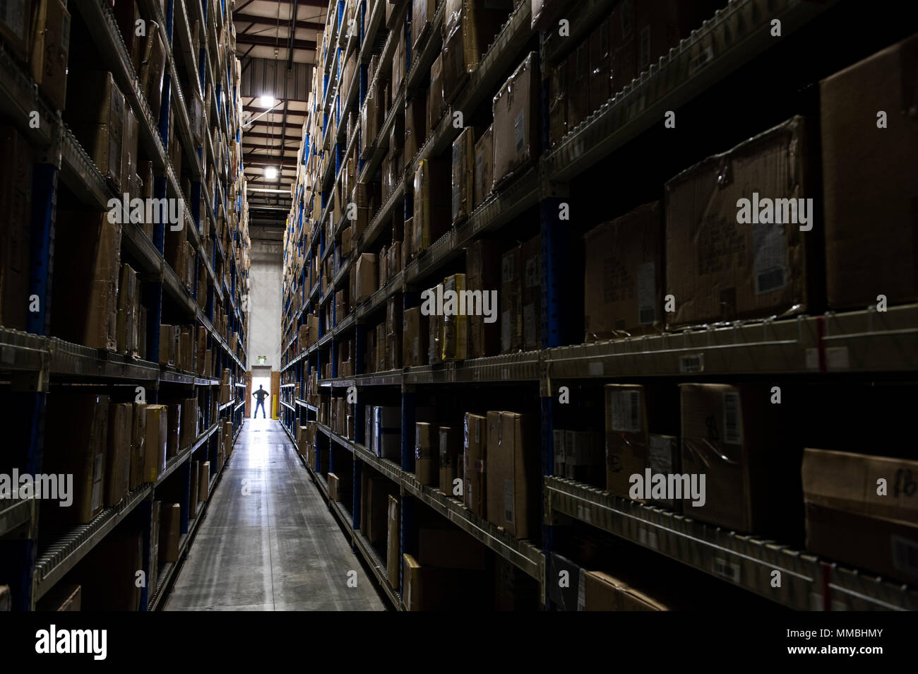 Single warehouse worker in between large racks of cardboard boxes on ...