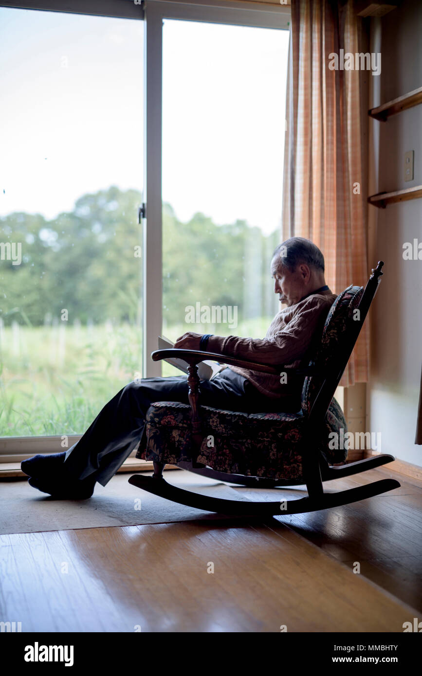 Elderly man sitting in rocking chair by a window, reading book Stock ...