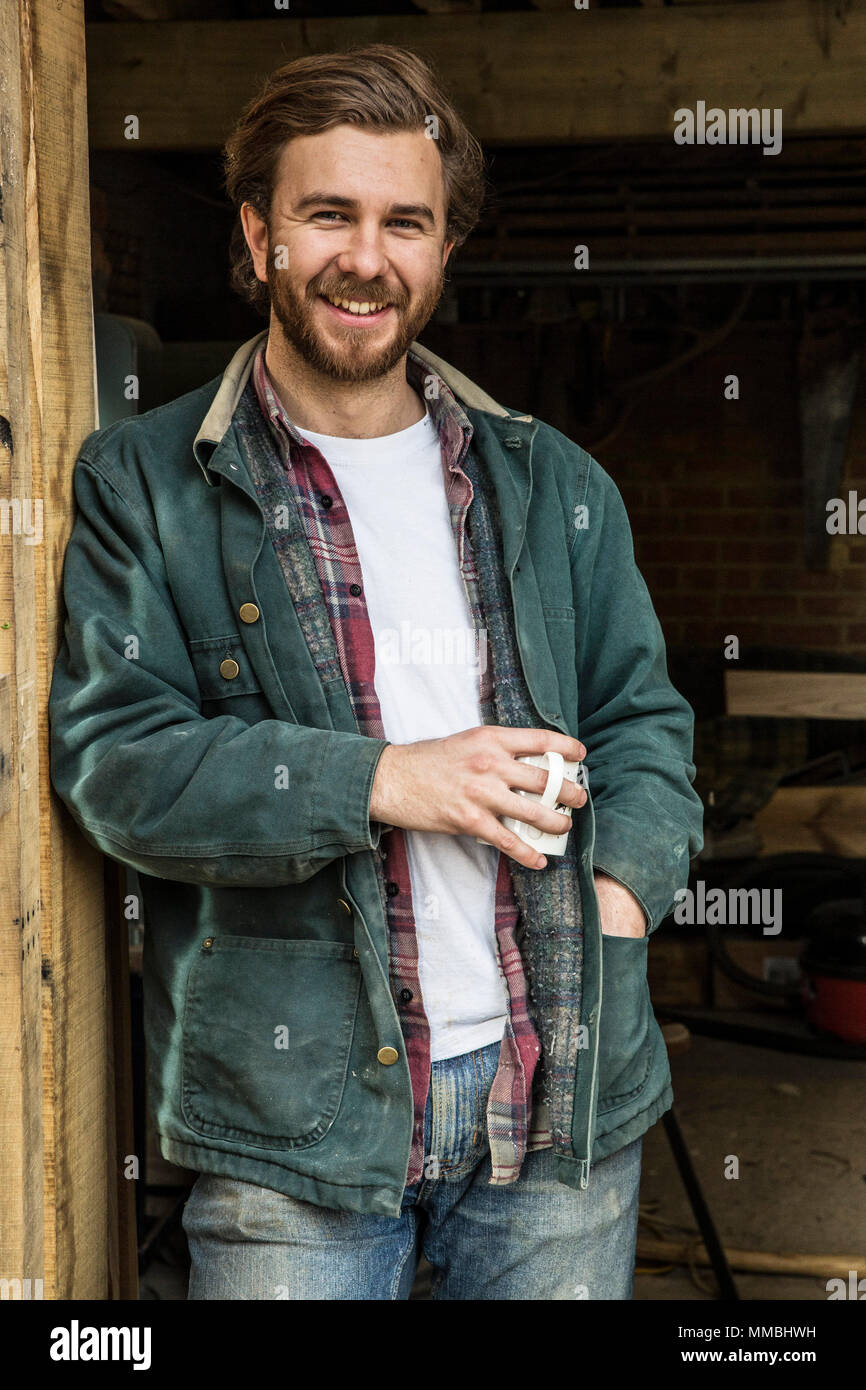 Bearded man standing in doorway of woodworking workshop, holding mug ...