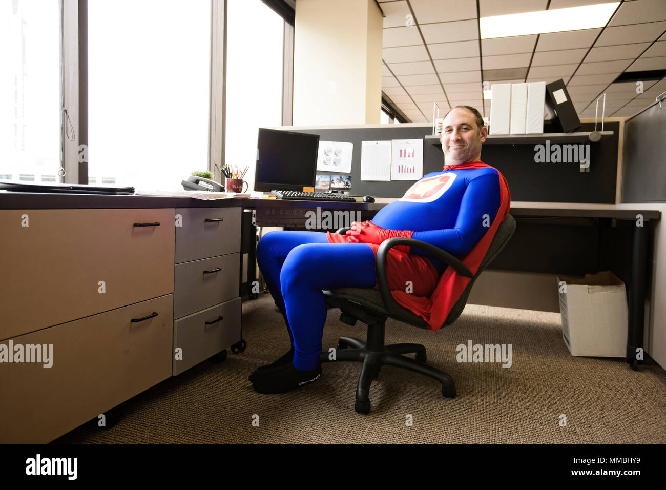 A self satisfied caucasian businessman super hero sits in his office ...