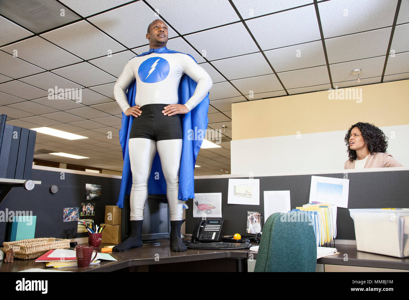 A black businessman office super hero stands on his cubicle desk ready ...