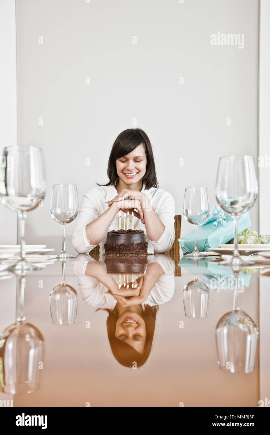 A woman seated at a table, hands clasped looking down, reflection on ...