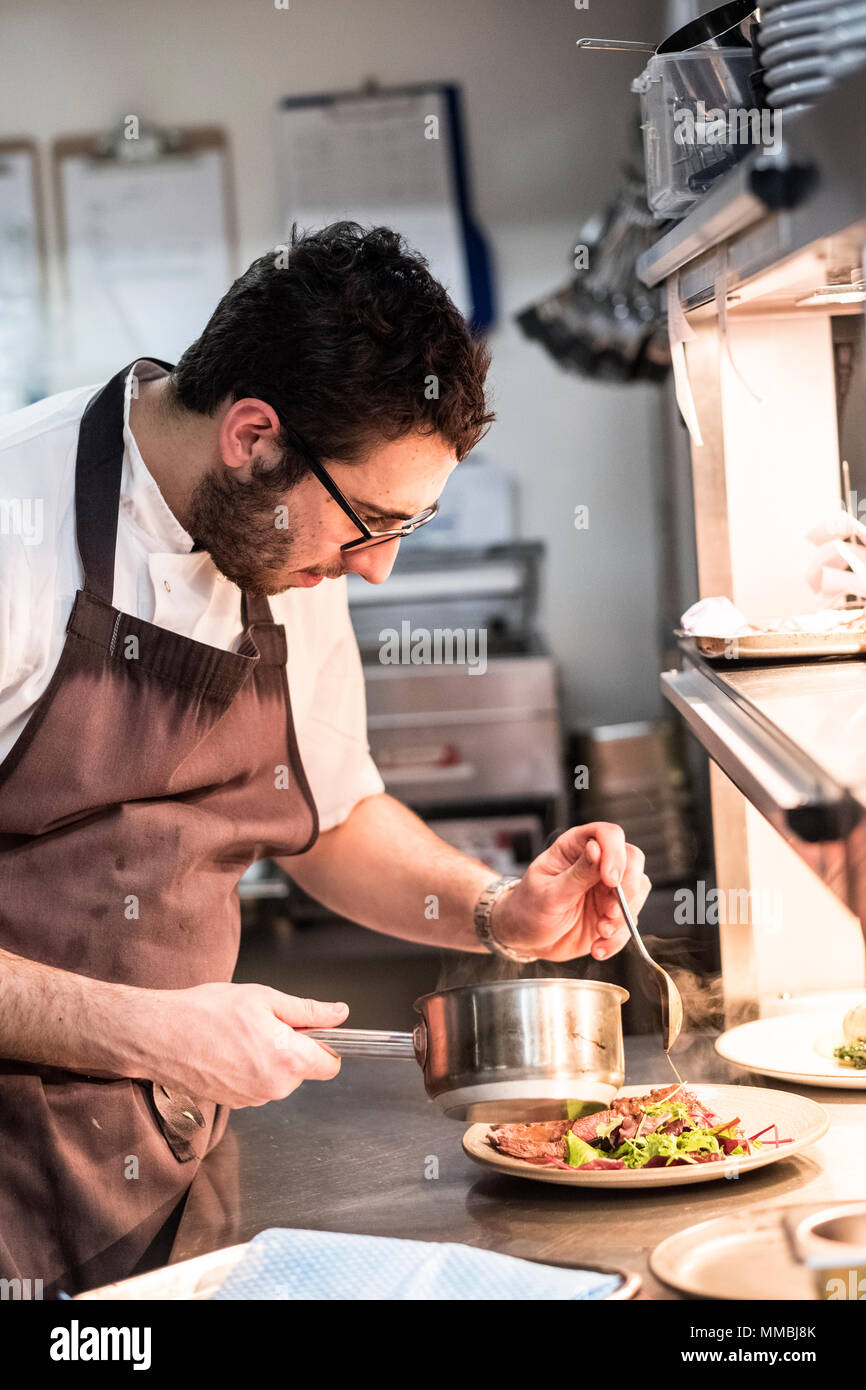 Bearded chef wearing glasses and apron standing in commercial kitchen ...