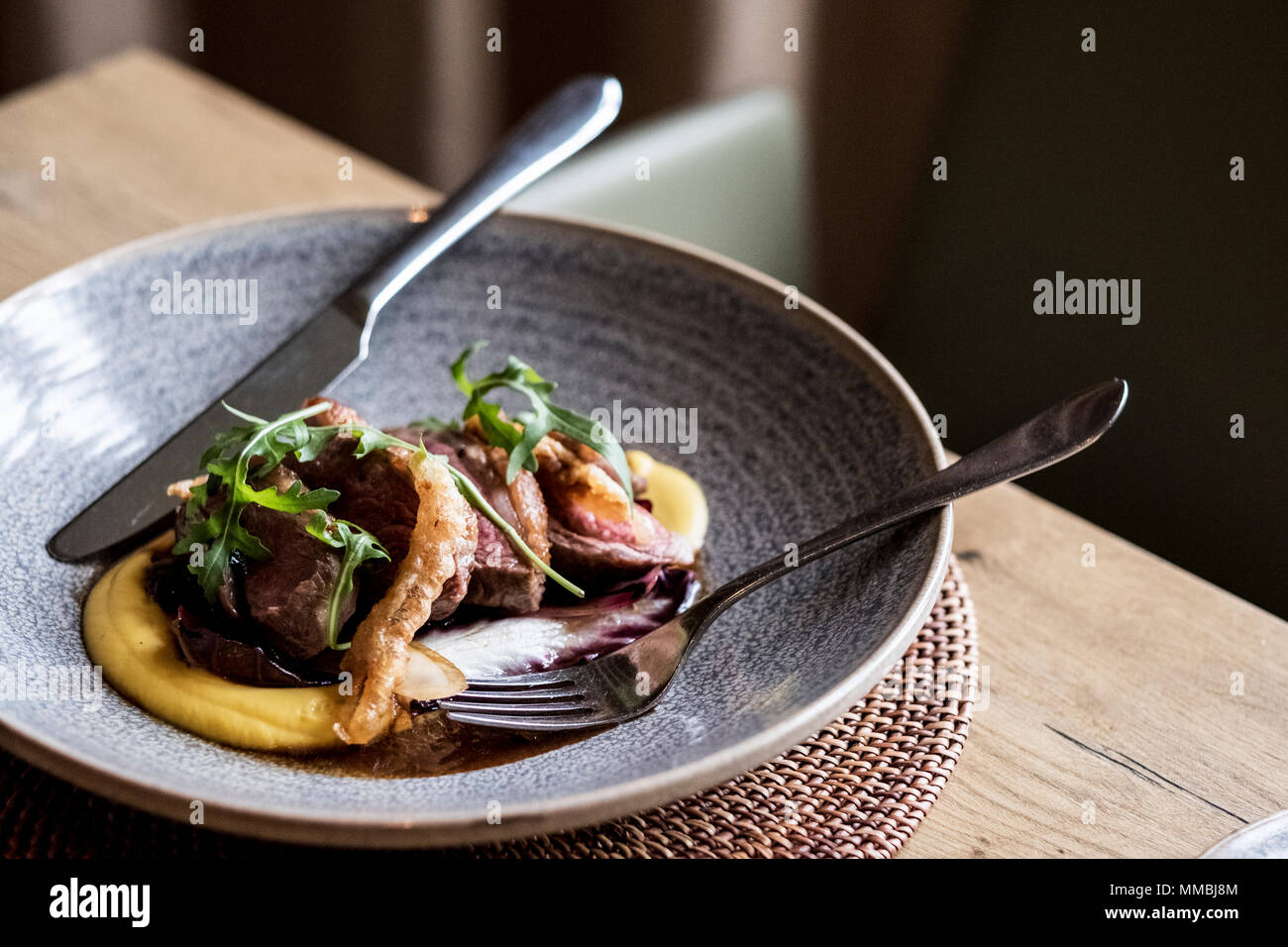 High angle close up of grey plate of meat with mashed potato, crackling ...