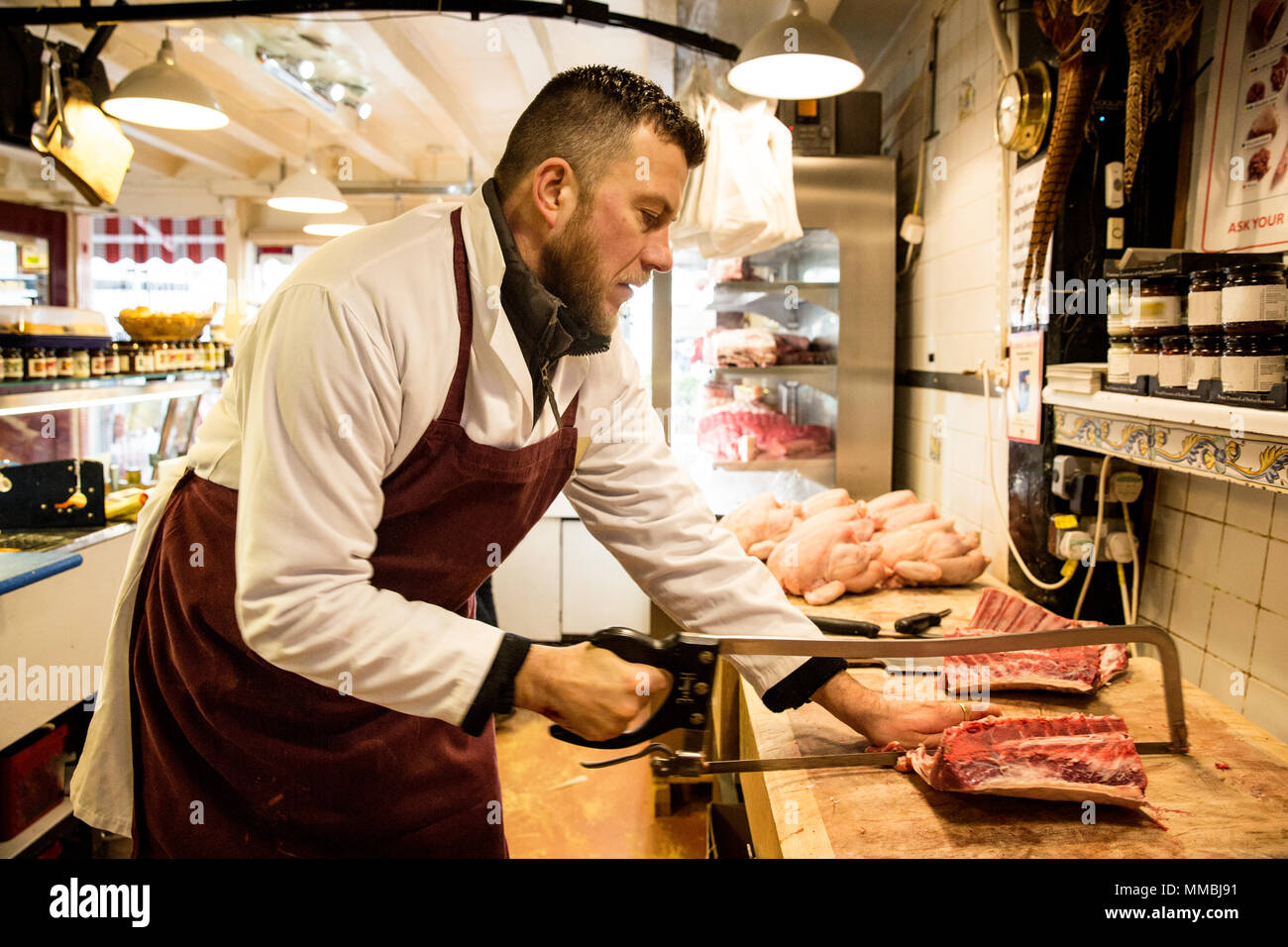 Man wearing apron standing at wooden butcher's block, butchering piece ...