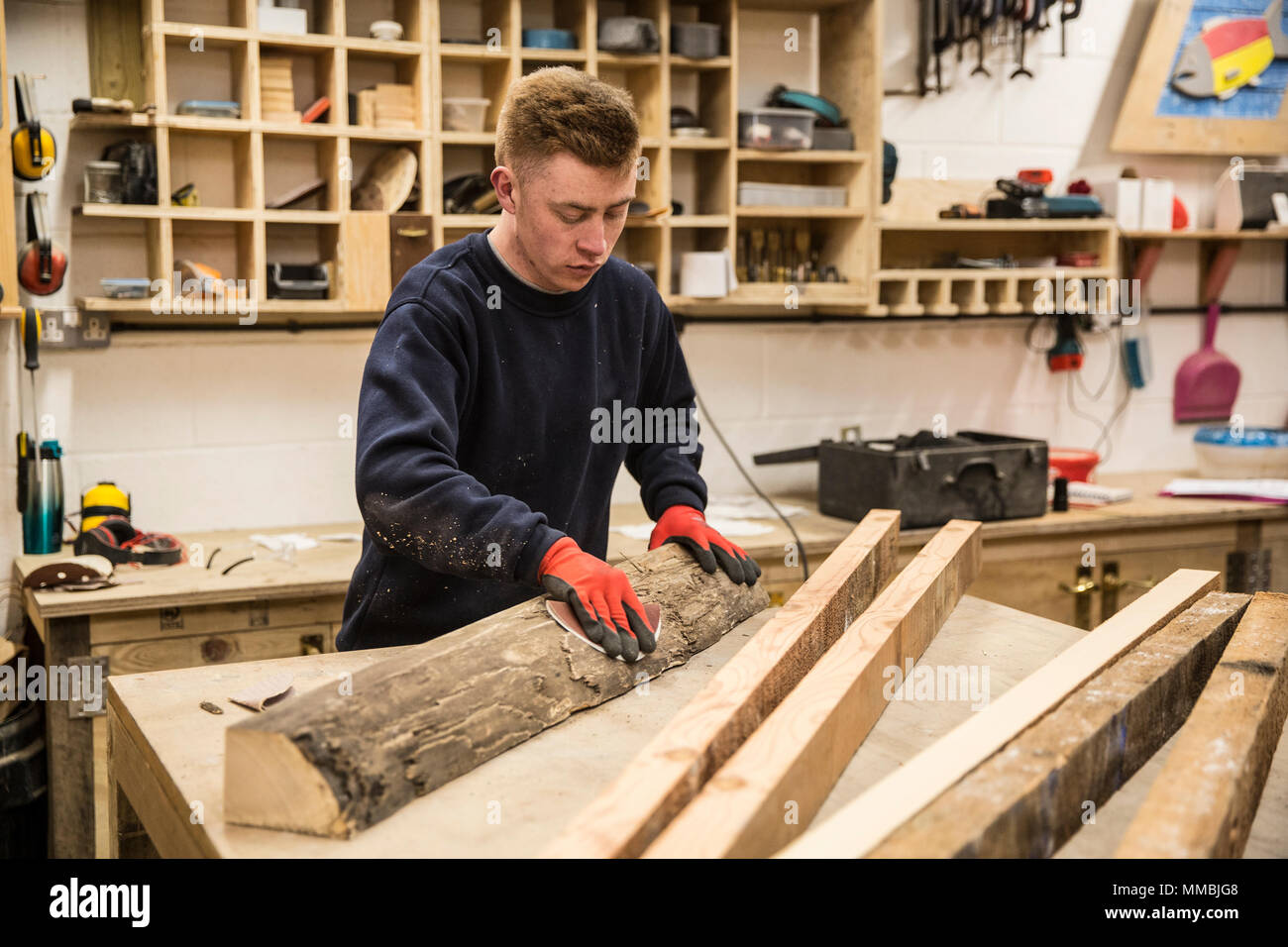 Man wearing work gloves standing at a workbench in a workshop, sanding ...