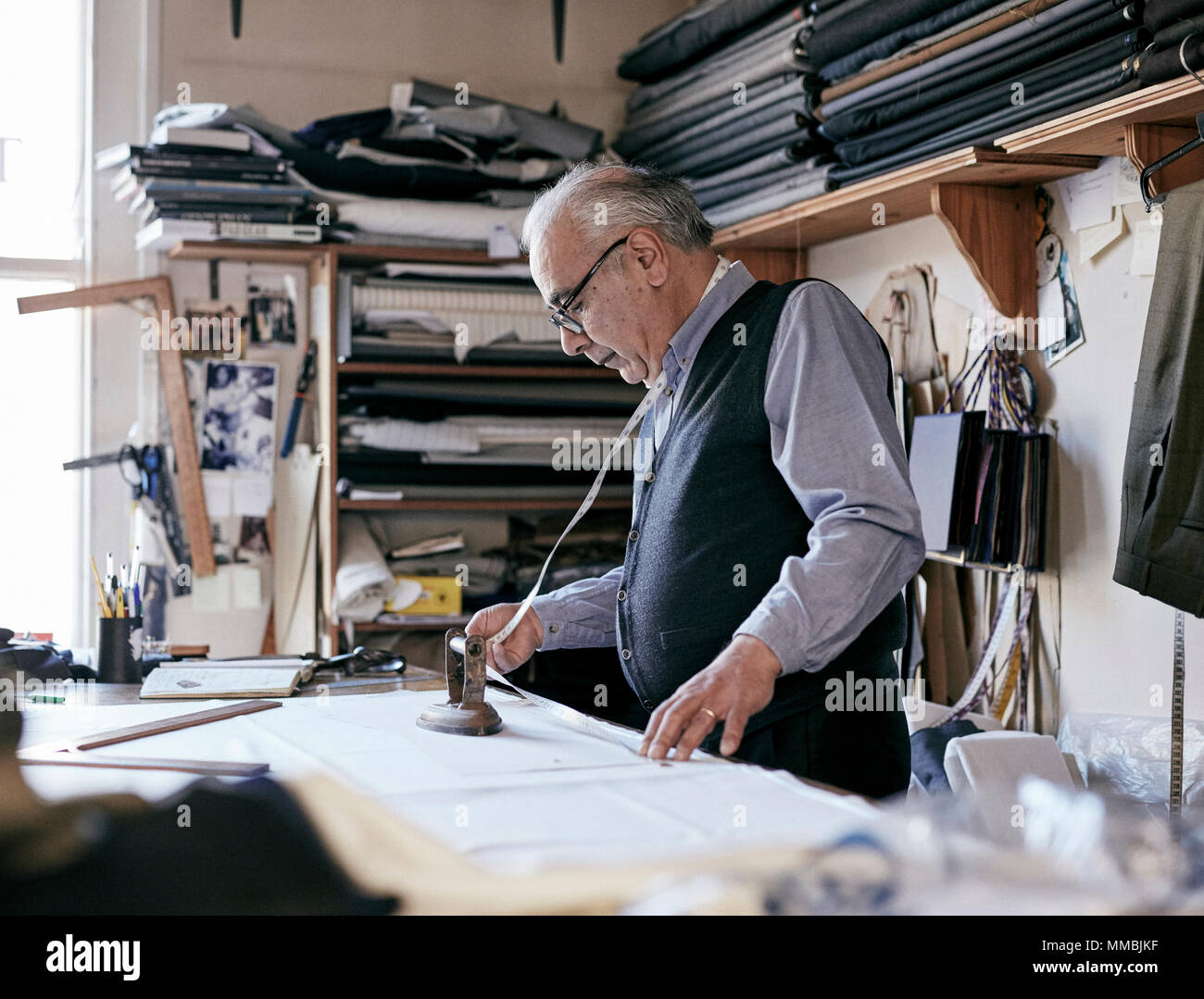 Tailor with measuring tape around neck working with material at bench ...