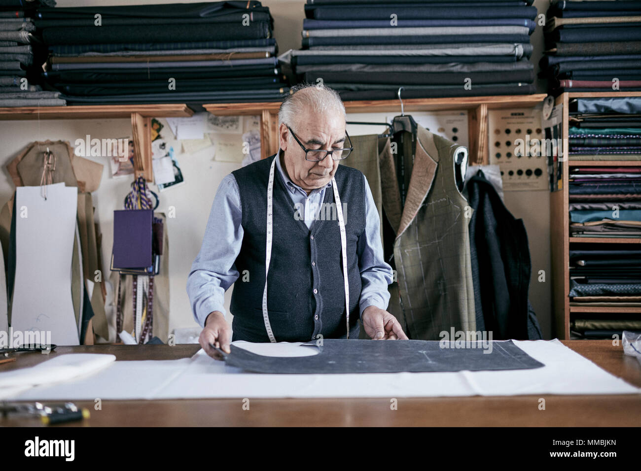 Tailor with measuring tape around neck working on a cut piece of fabric ...