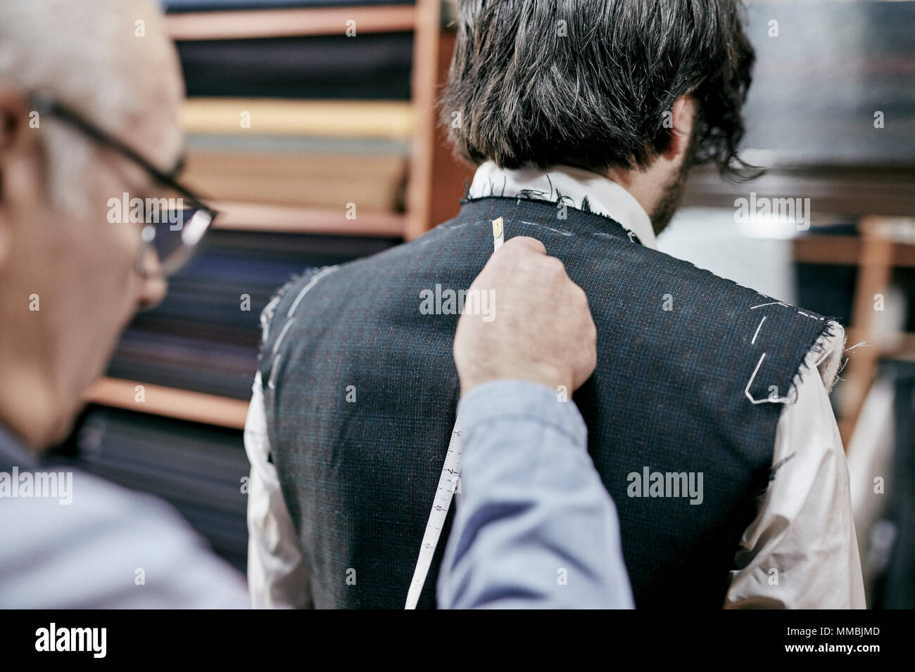 Tailor using measuring tape on a suit jacket, fitting the garment on a ...