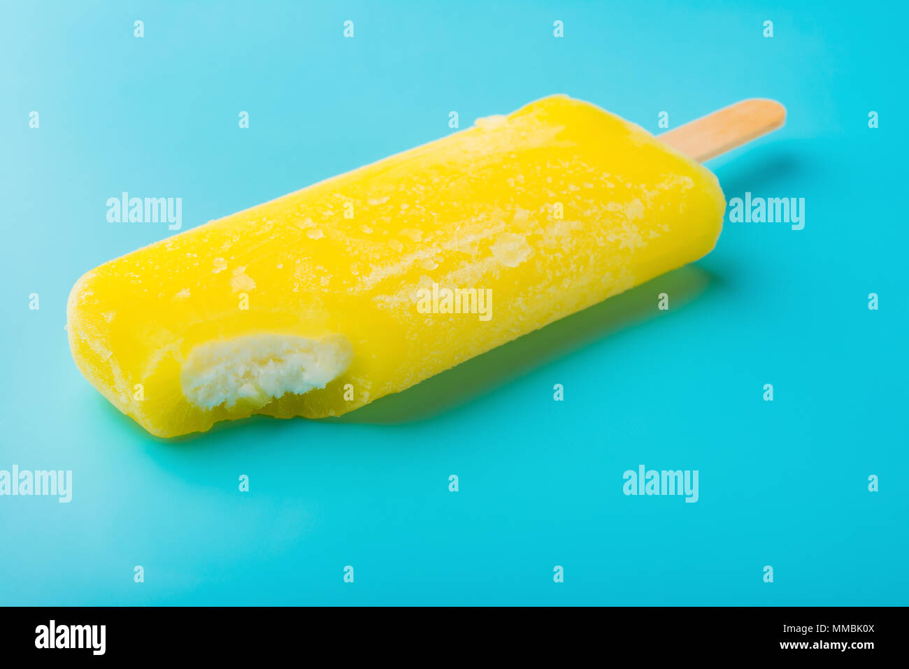 side view yellow popsicle with a bite on a blue background Stock Photo ...