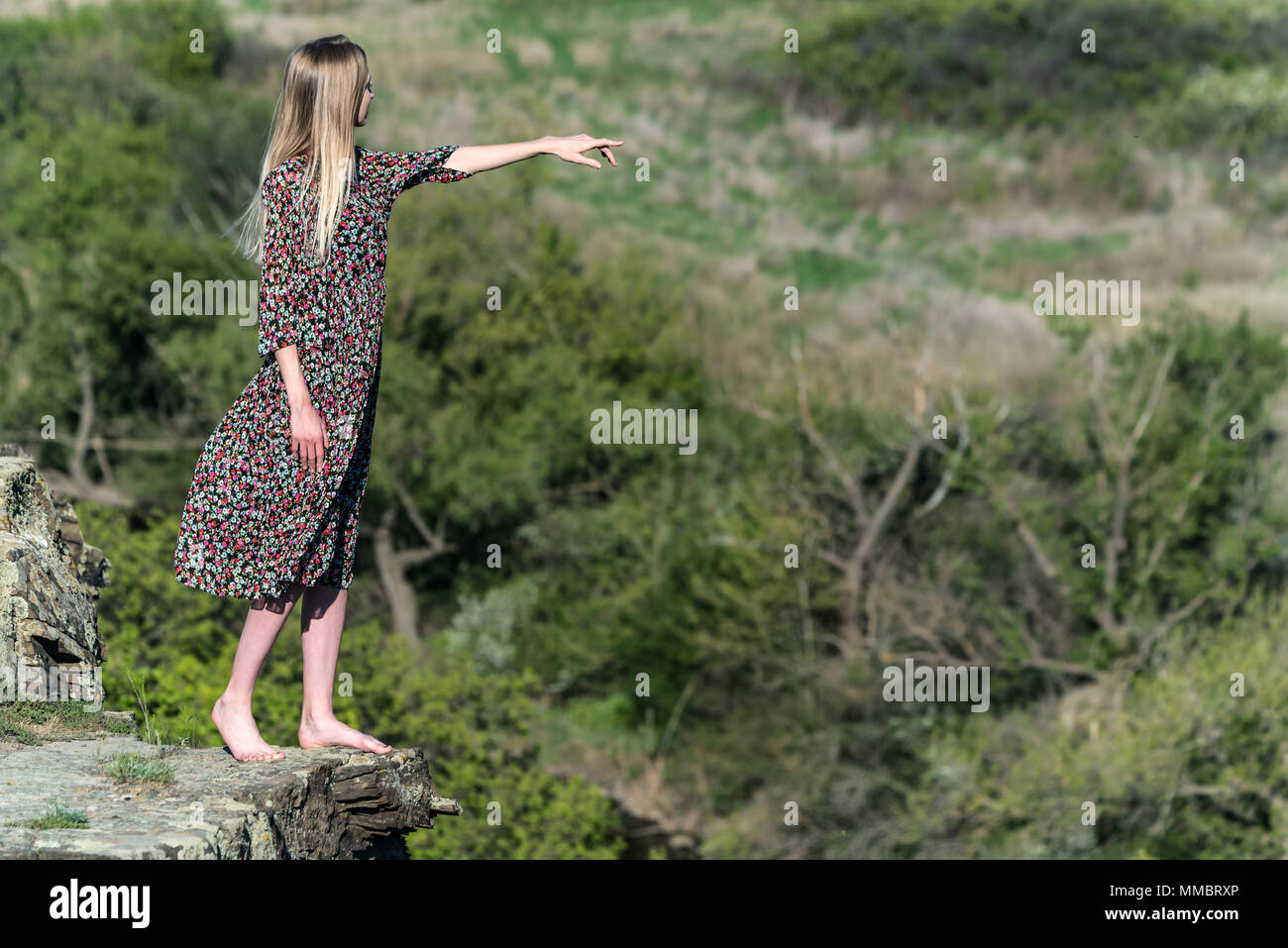Beautiful girl in dress on rock points in disance Stock Photo - Alamy