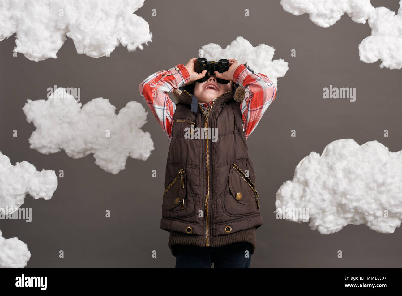 boy dressed as an airplane pilot stands between the clouds and looks ...