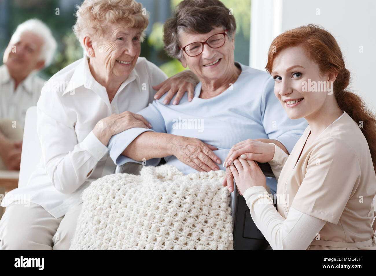 Two elder women and friendly nurse are smiling during meeting in common ...