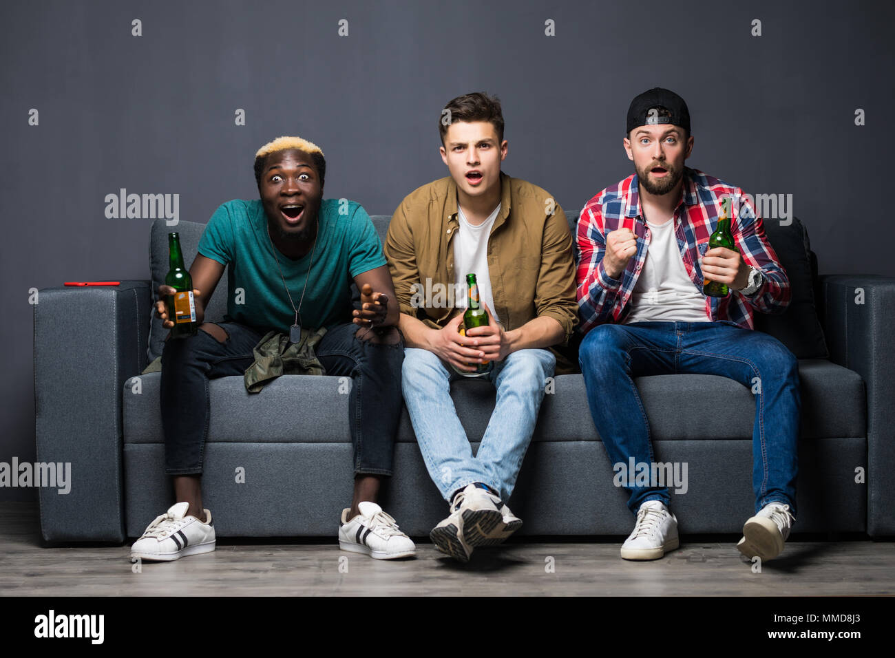group of exited men sitting together on couch, watching television ...